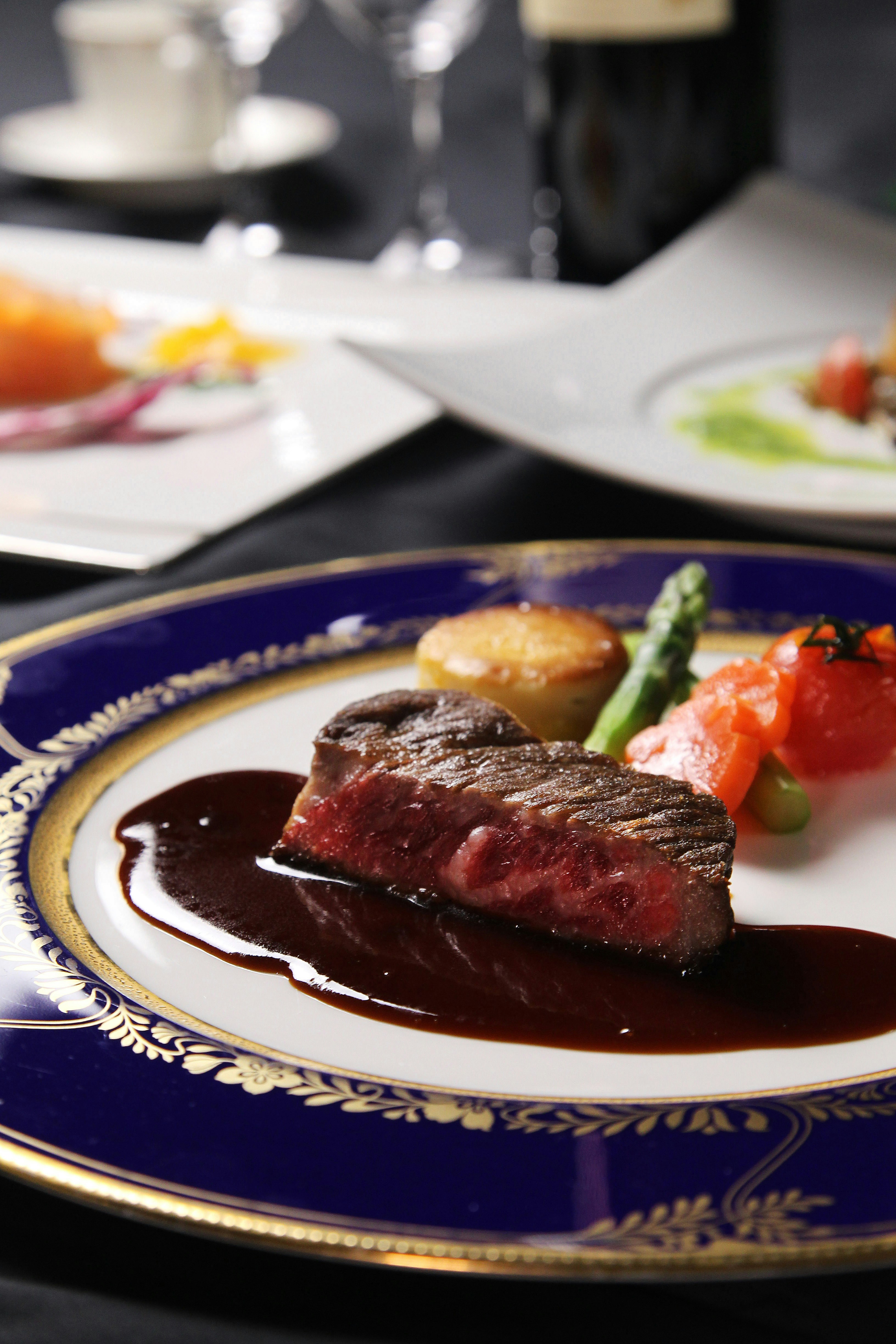 Juicy steak with rich sauce, accompanied by vegetables and garnished elegantly on a decorative plate.