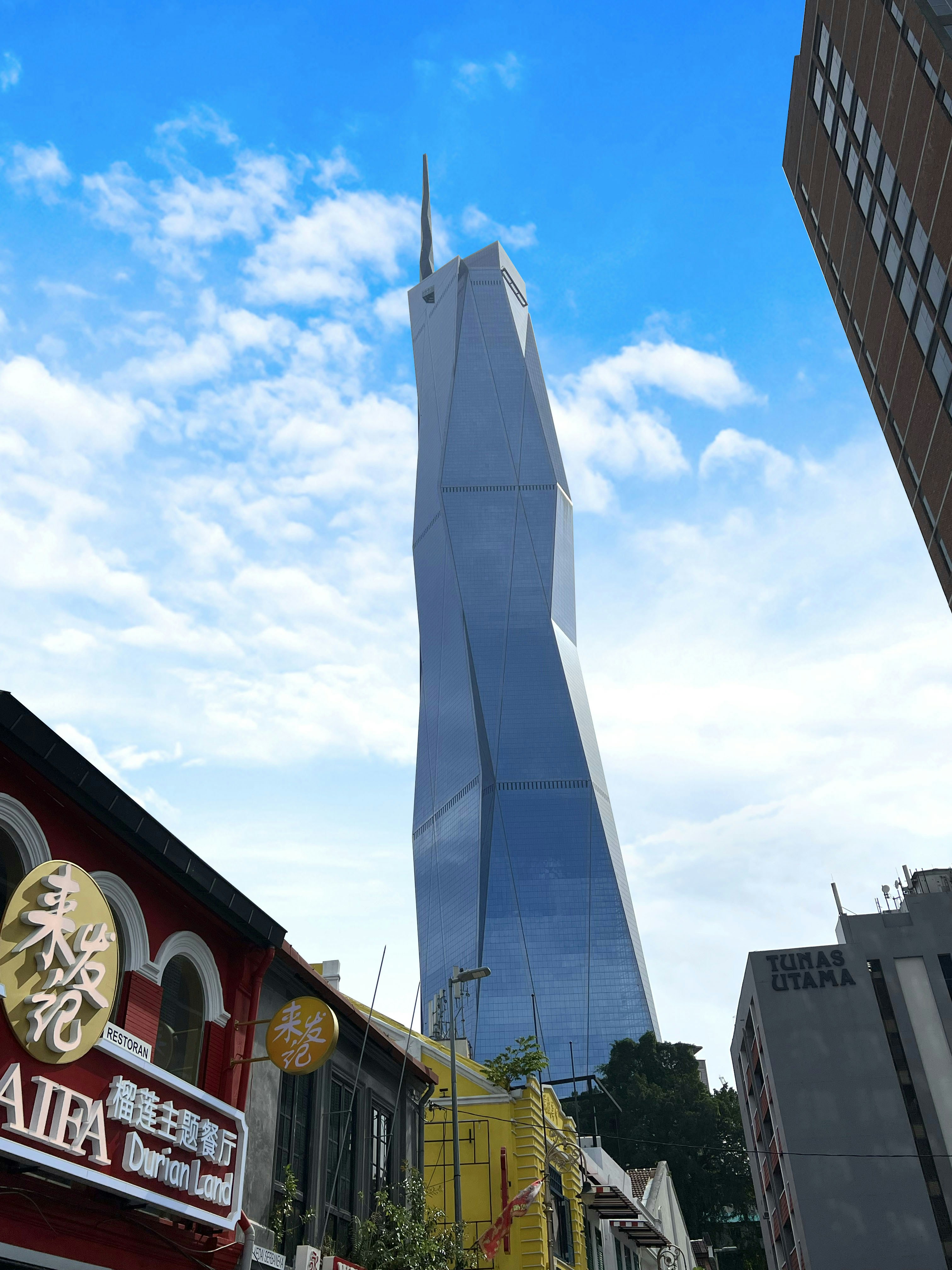 Merdeka 118 tower rises above city buildings under a vibrant blue sky.