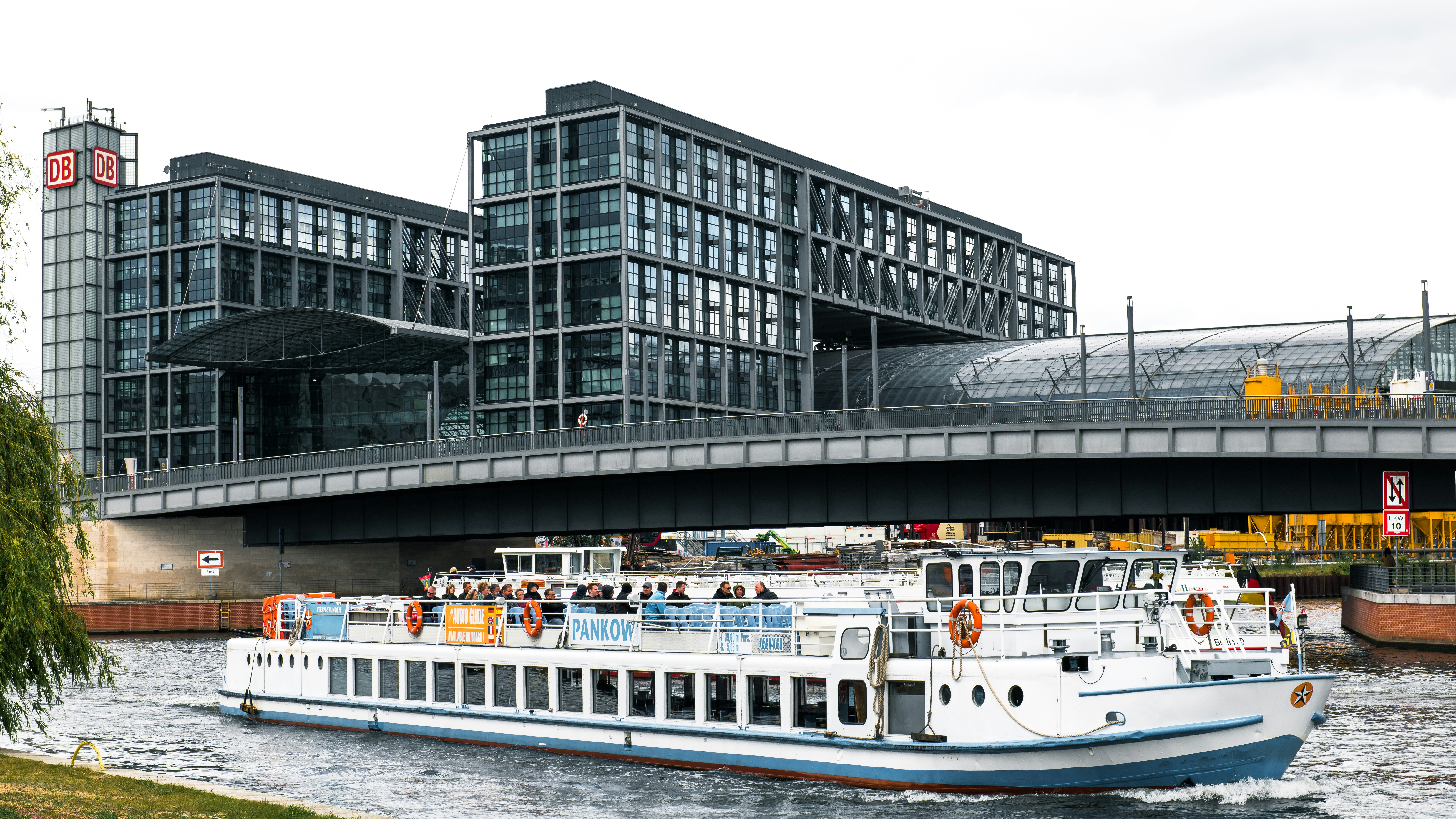 Tourist boat passing beneath a contemporary bridge with a modern glass building in the background.
