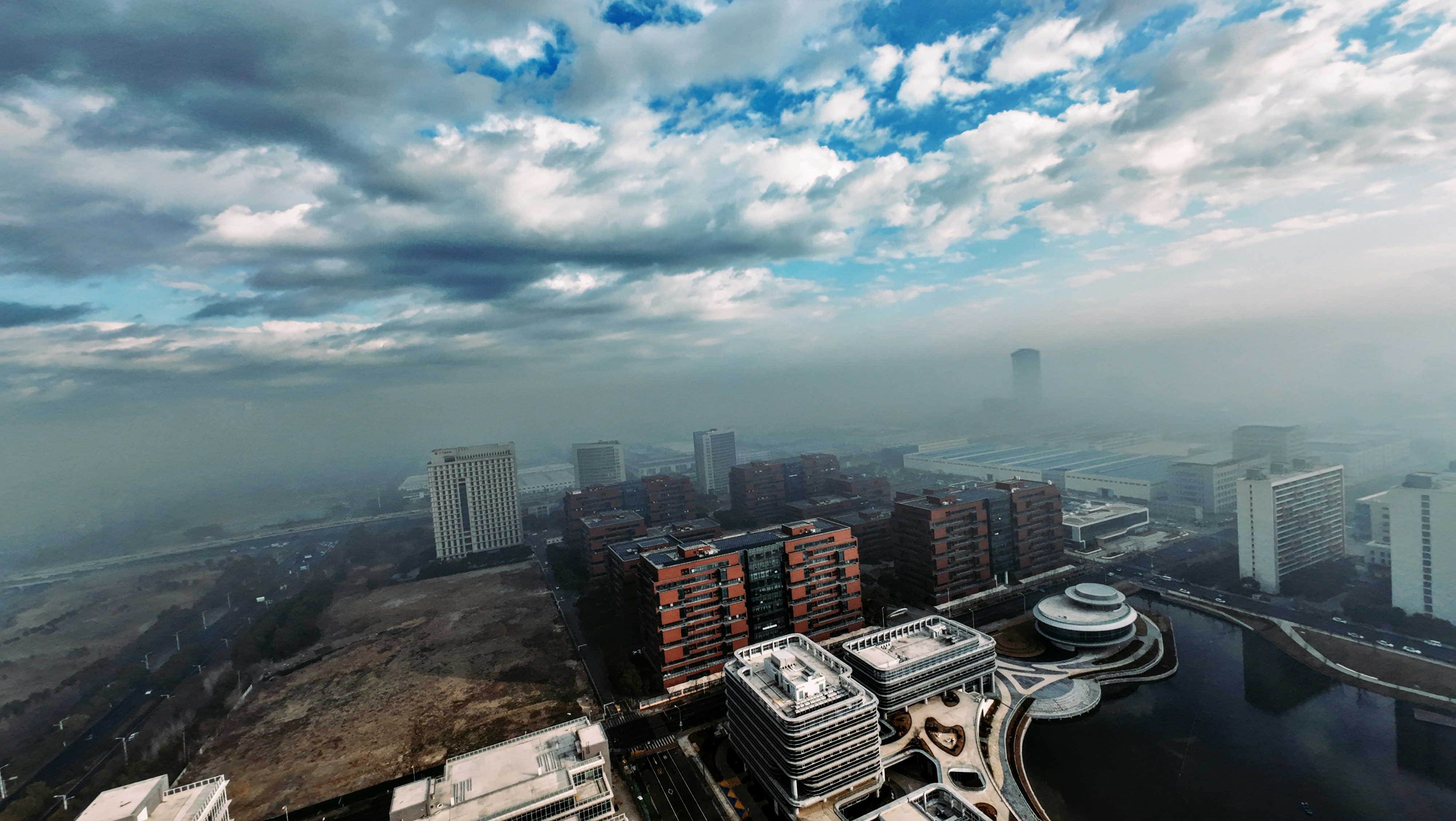Cityscape with modern buildings enveloped in mist beneath a dramatic cloudy sky.