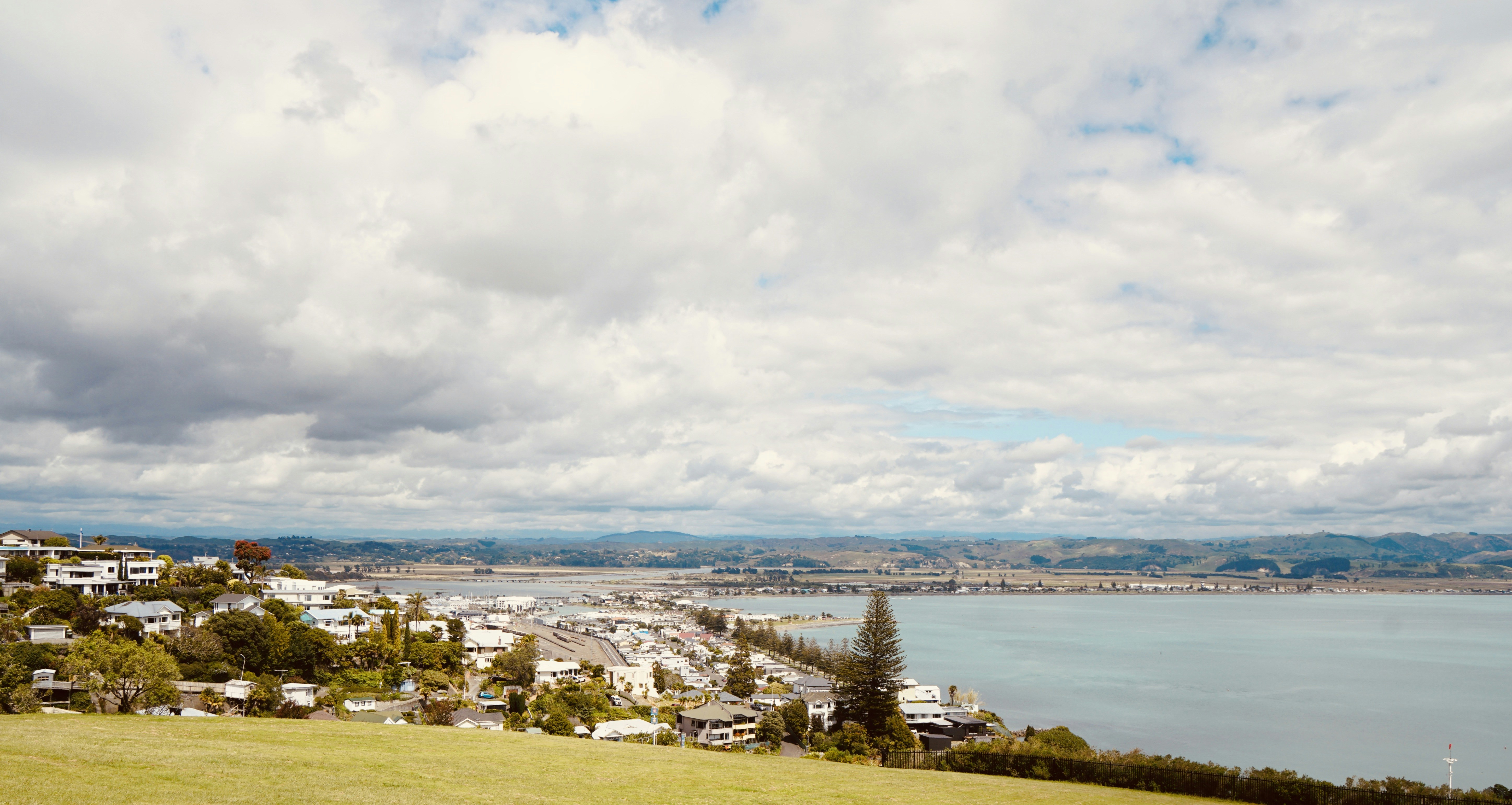 Coastal town with houses overlooking a tranquil sea under a cloudy sky.