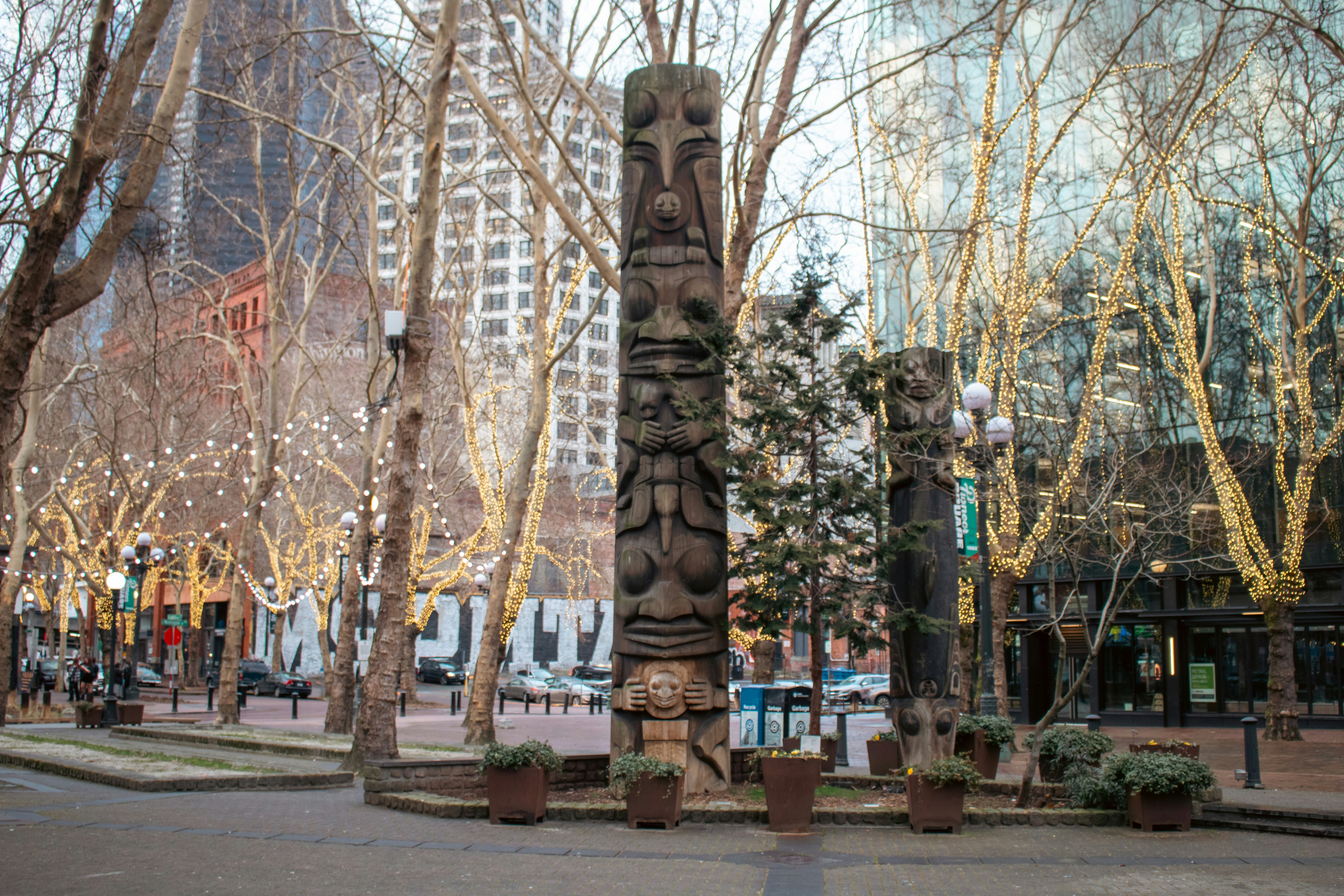 Totem poles stand in a public park with buildings. photo – Free City ...