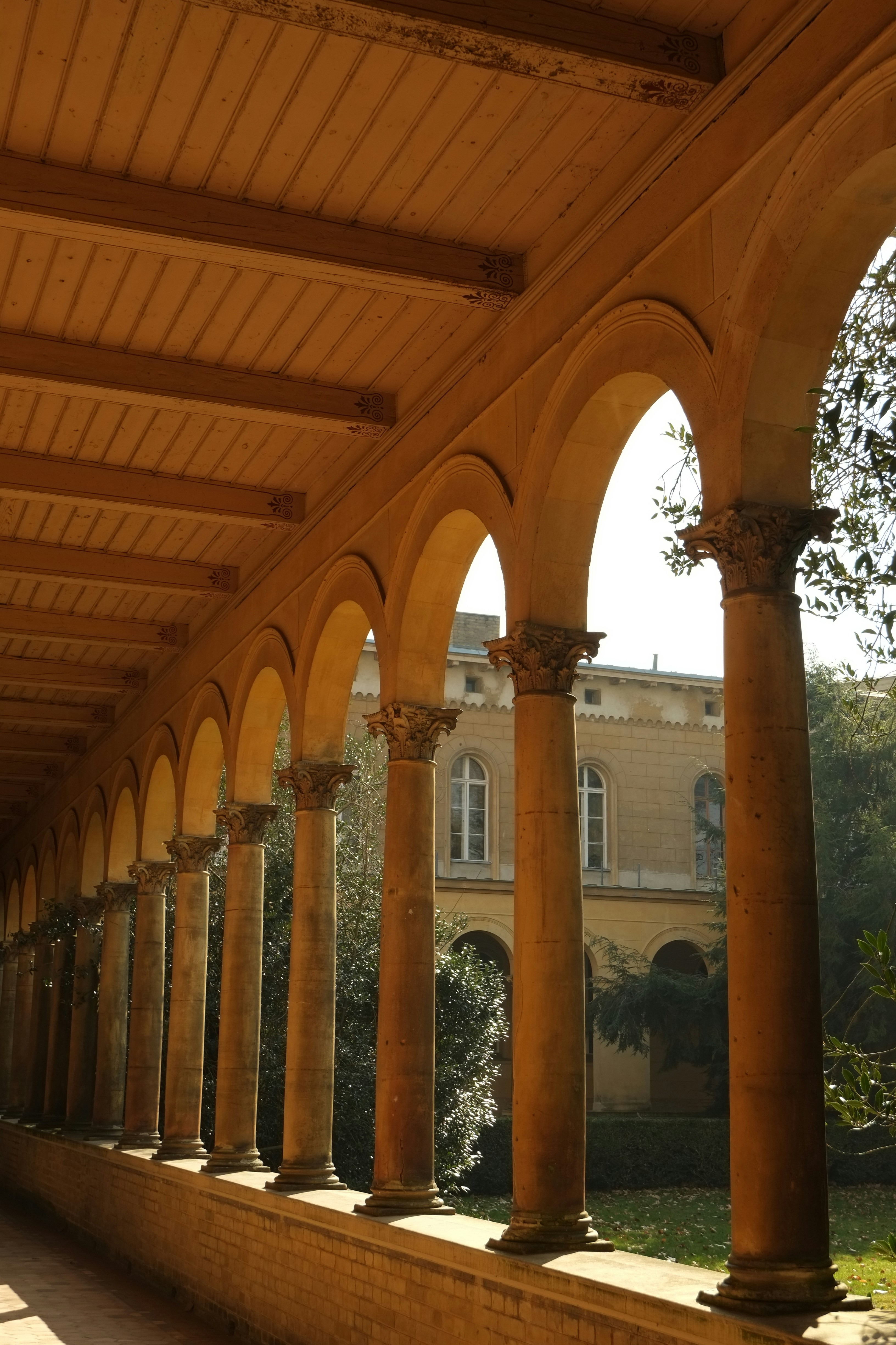 A covered walkway with arched columns and a building. photo – Free ...