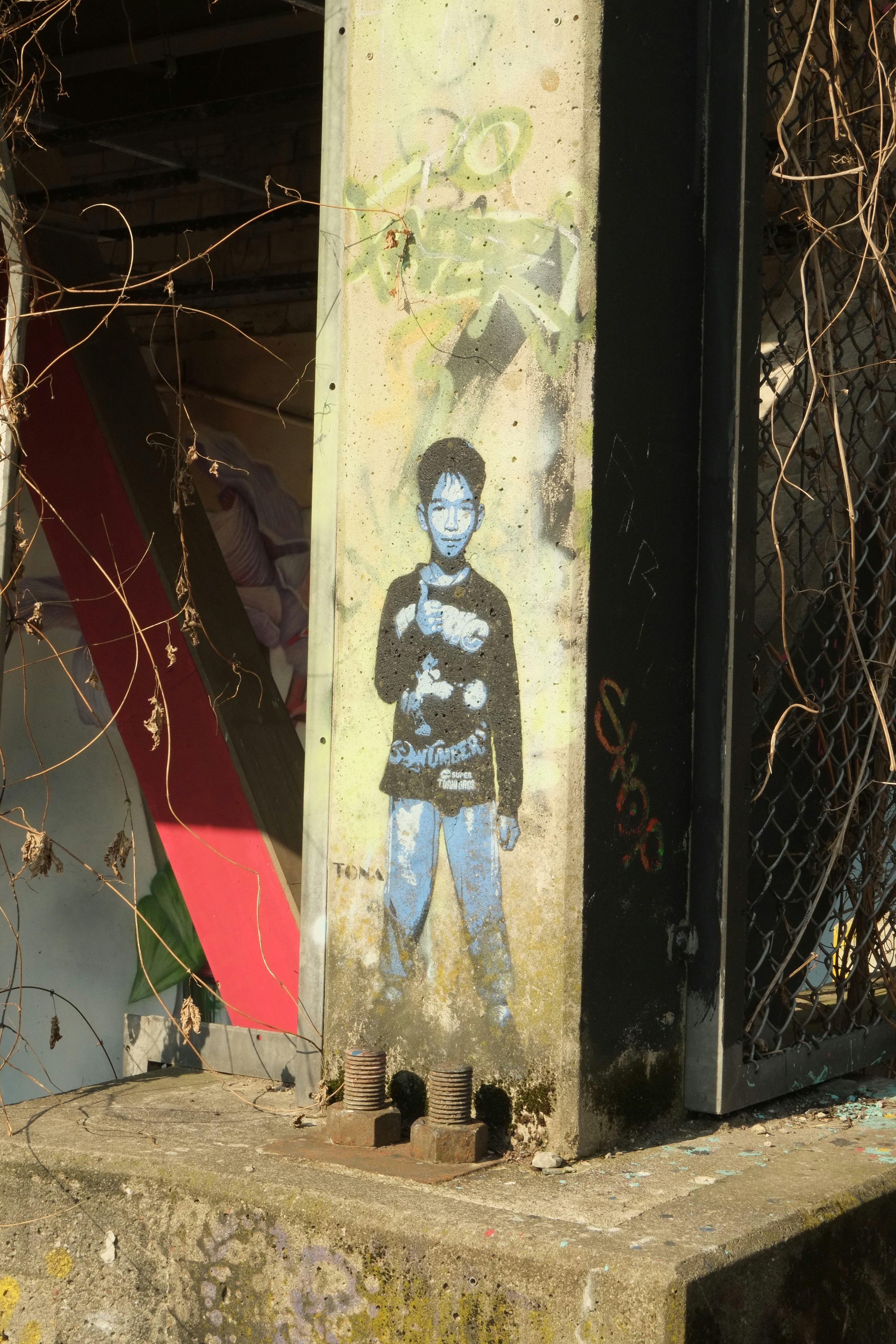 Blue Figure on a Weathered Pillar, Graffiti Amid Ivy and Steel