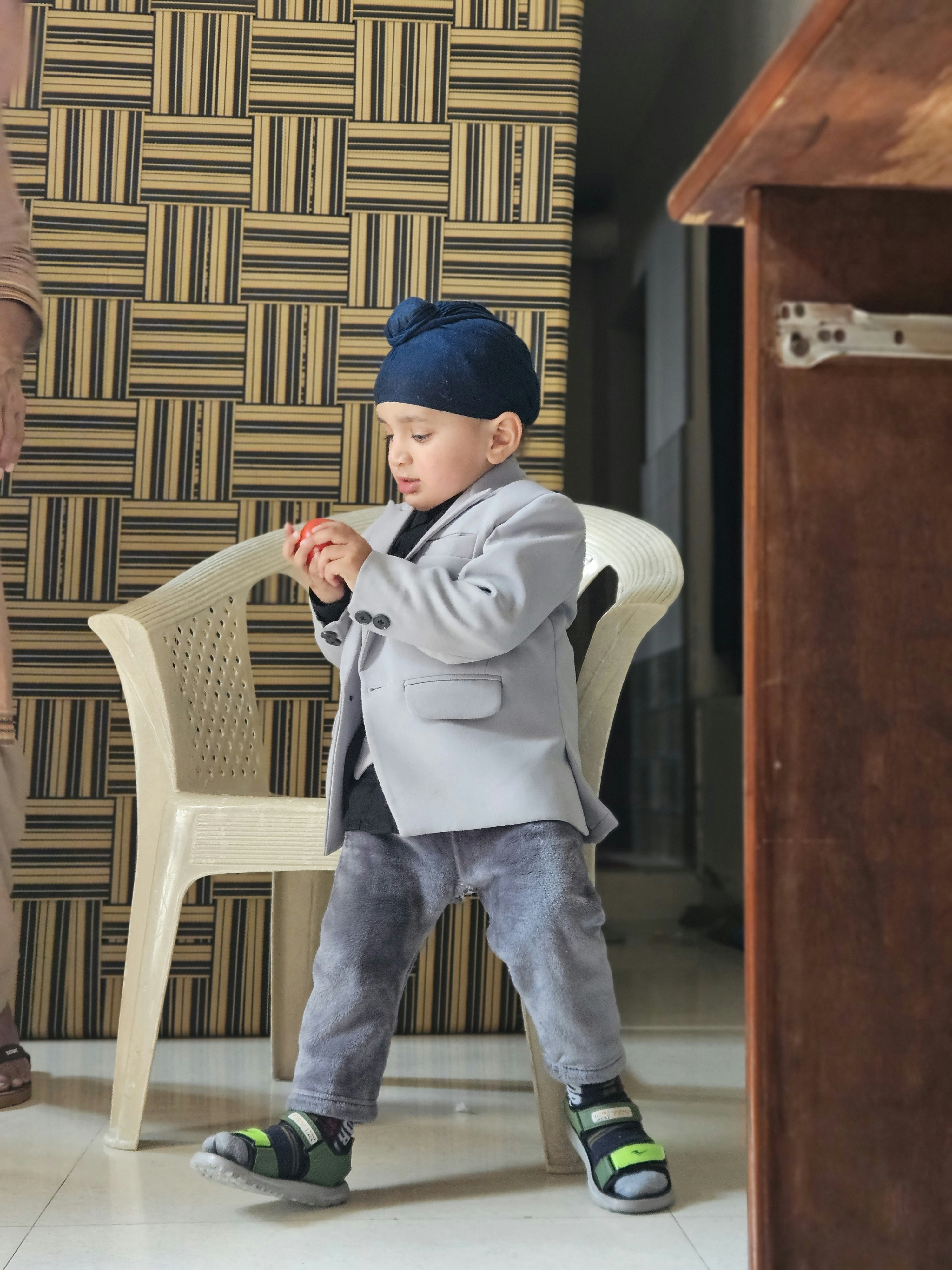 Tiny Gentleman in a Gray Blazer Examines a Red Toy in a Quiet Hall