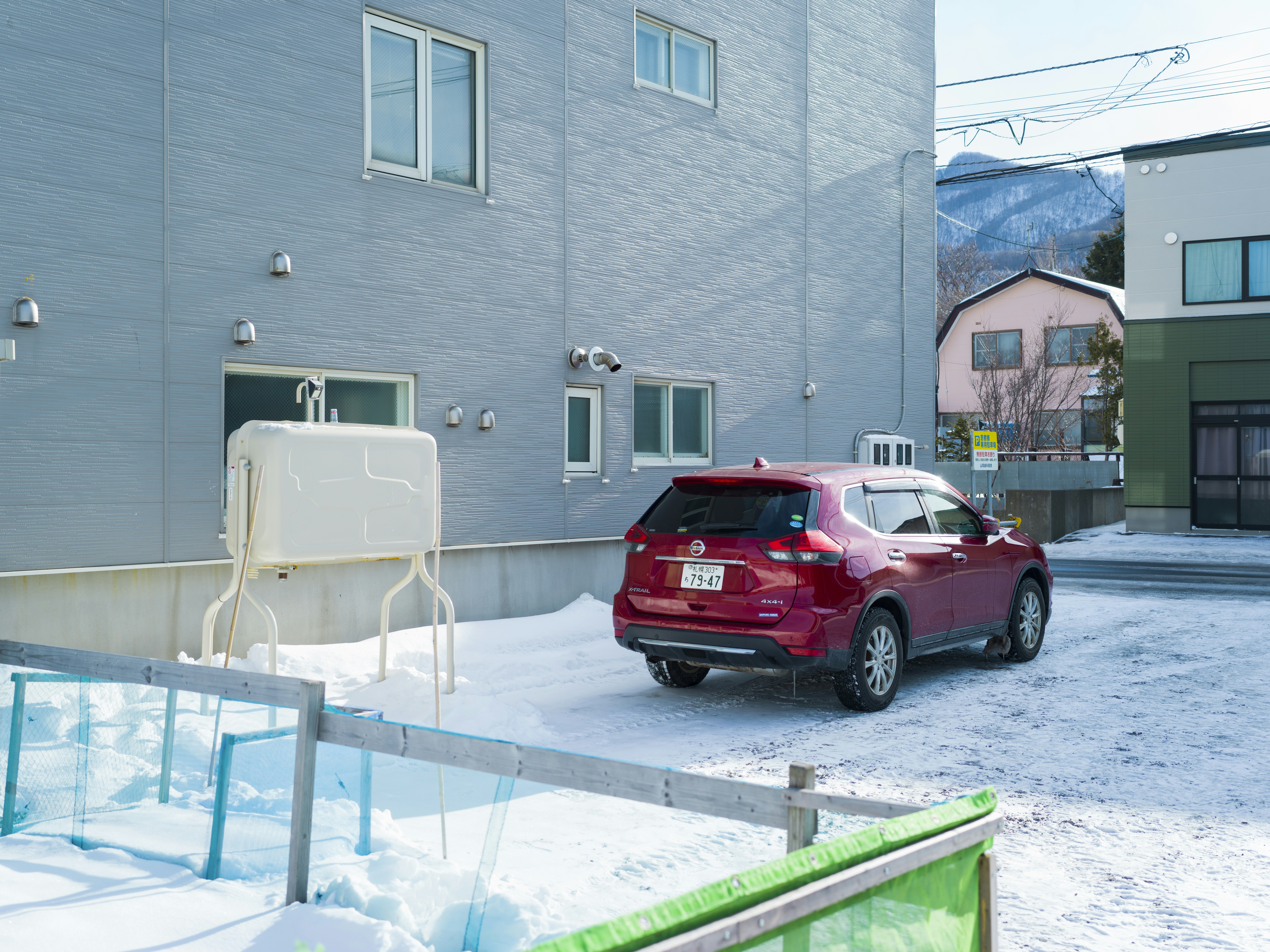 Red SUV parked in a snowy urban area beside gray buildings.