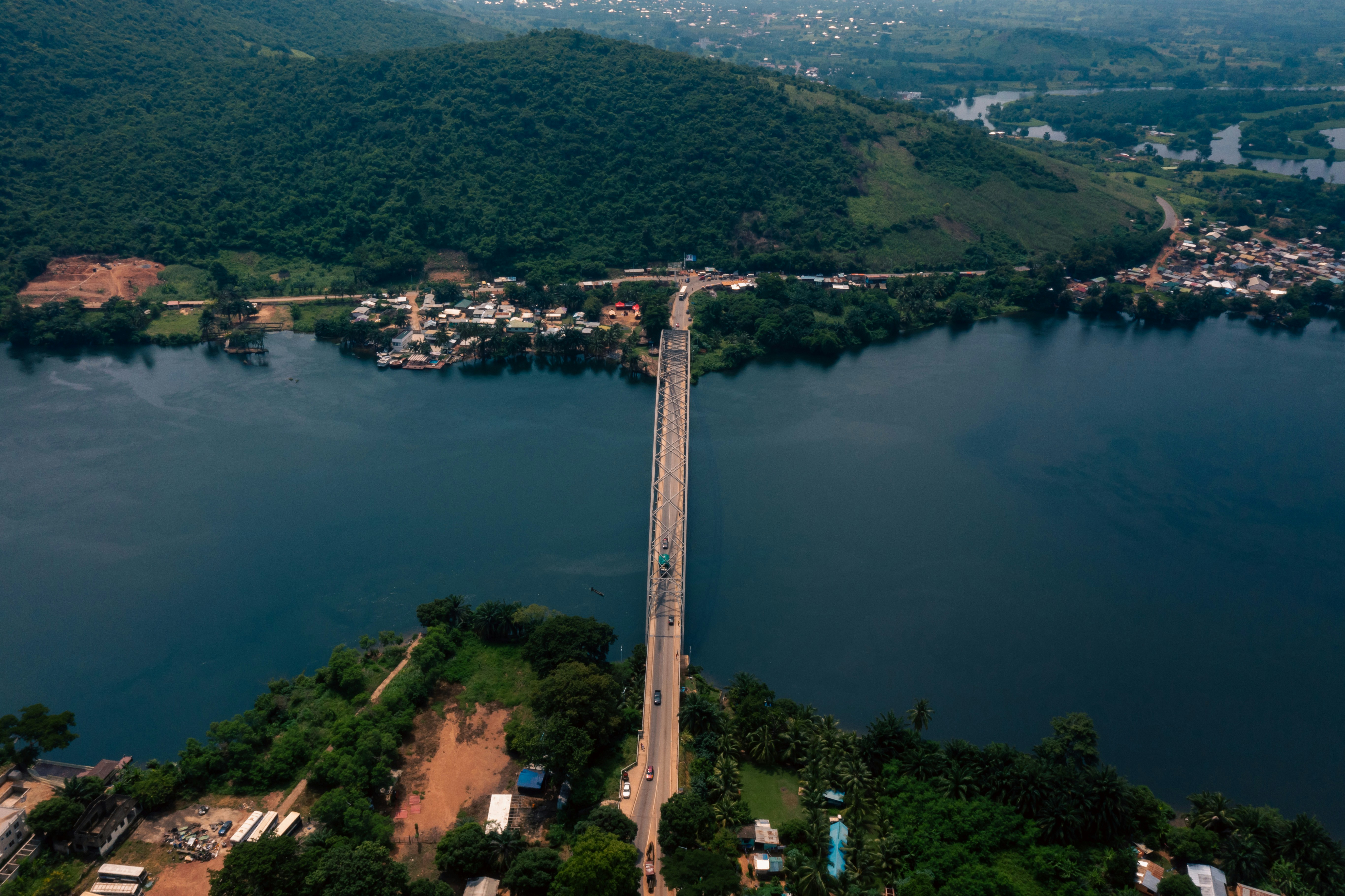 Long bridge stretching across a tranquil river flanked by lush green hills.