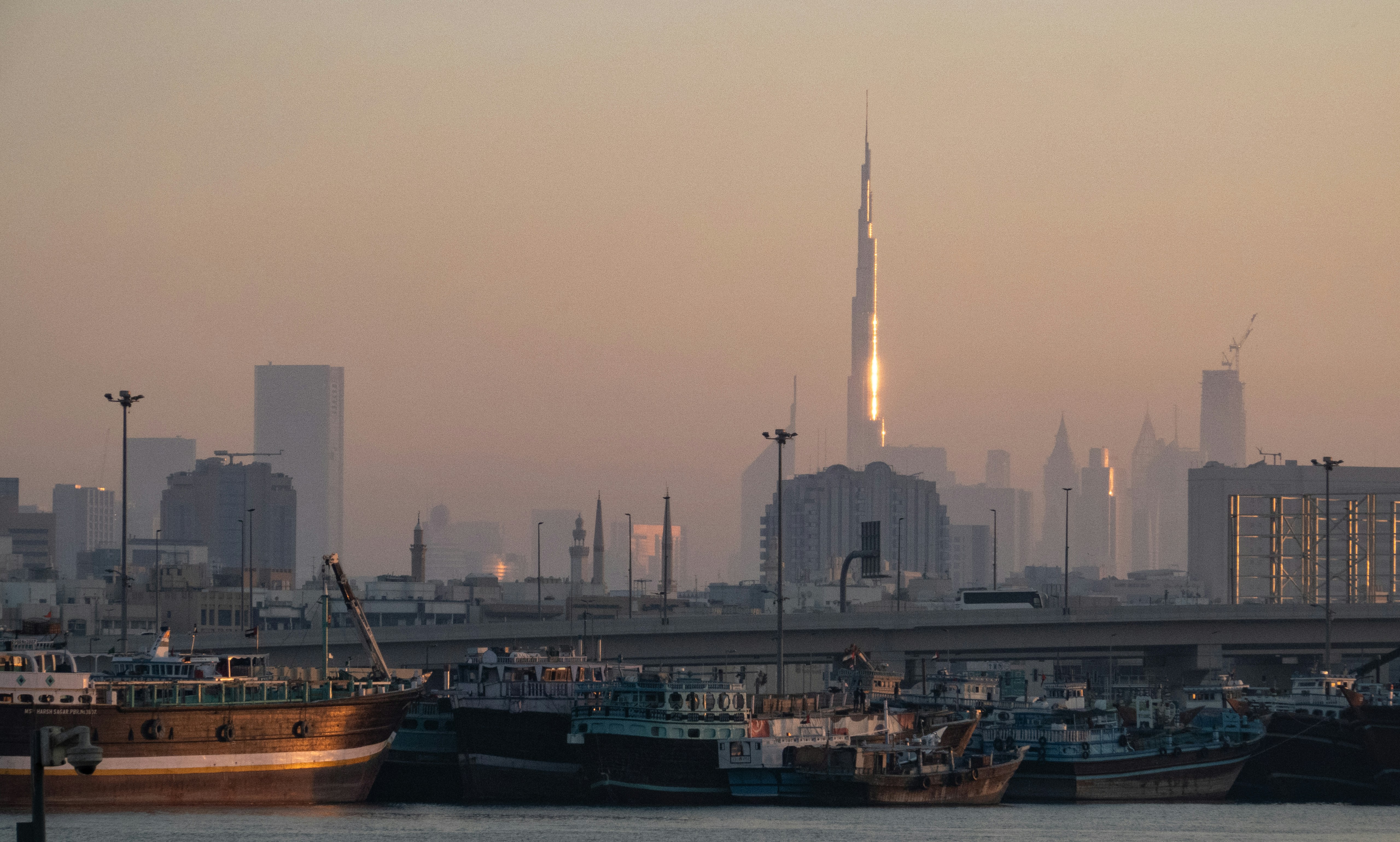 Distant view of the Burj Khalifa glowing in the sunset amidst a hazy cityscape.