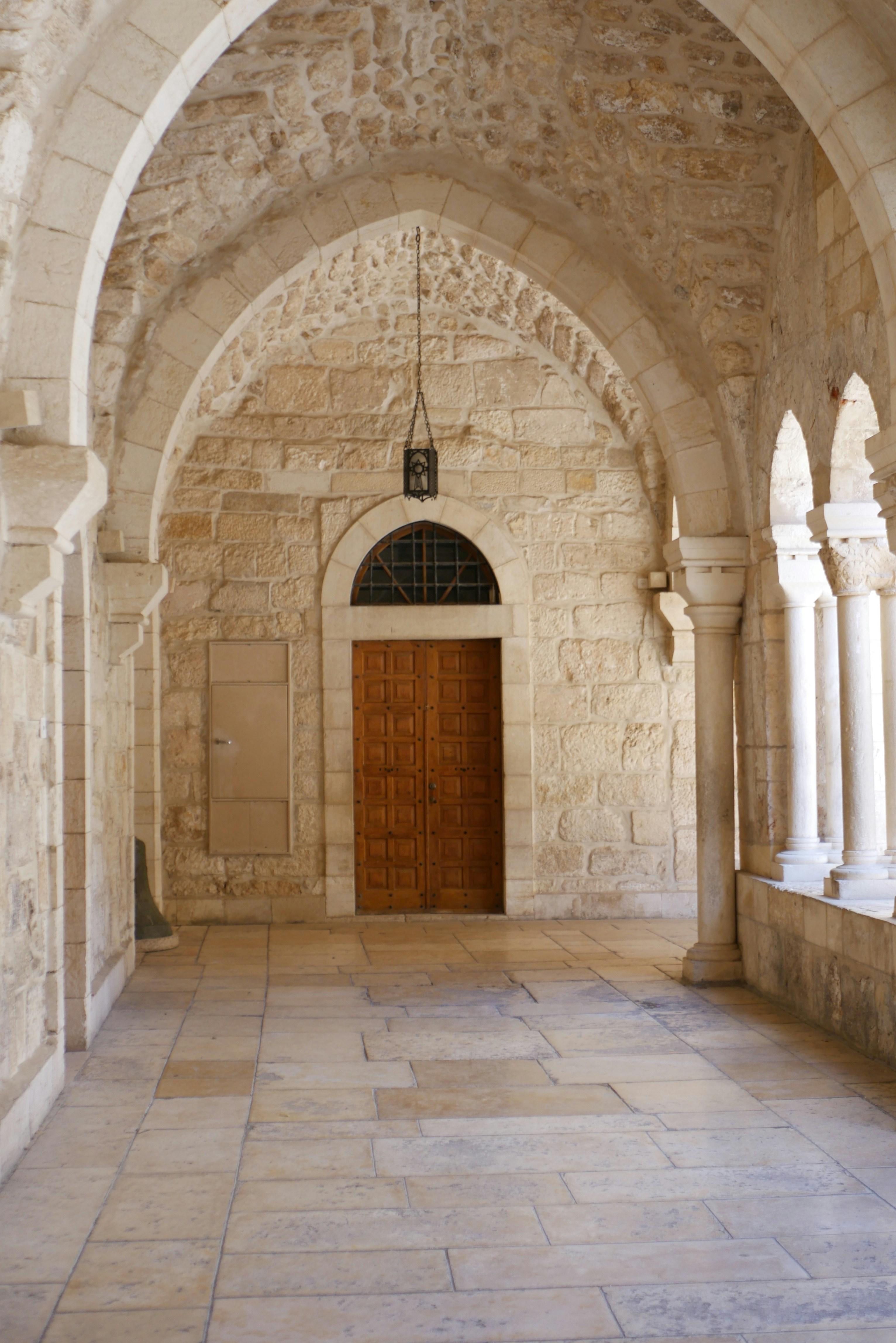 Doorway Through Time: Central Wooden Portal Framed by Sunlit Stone Arches