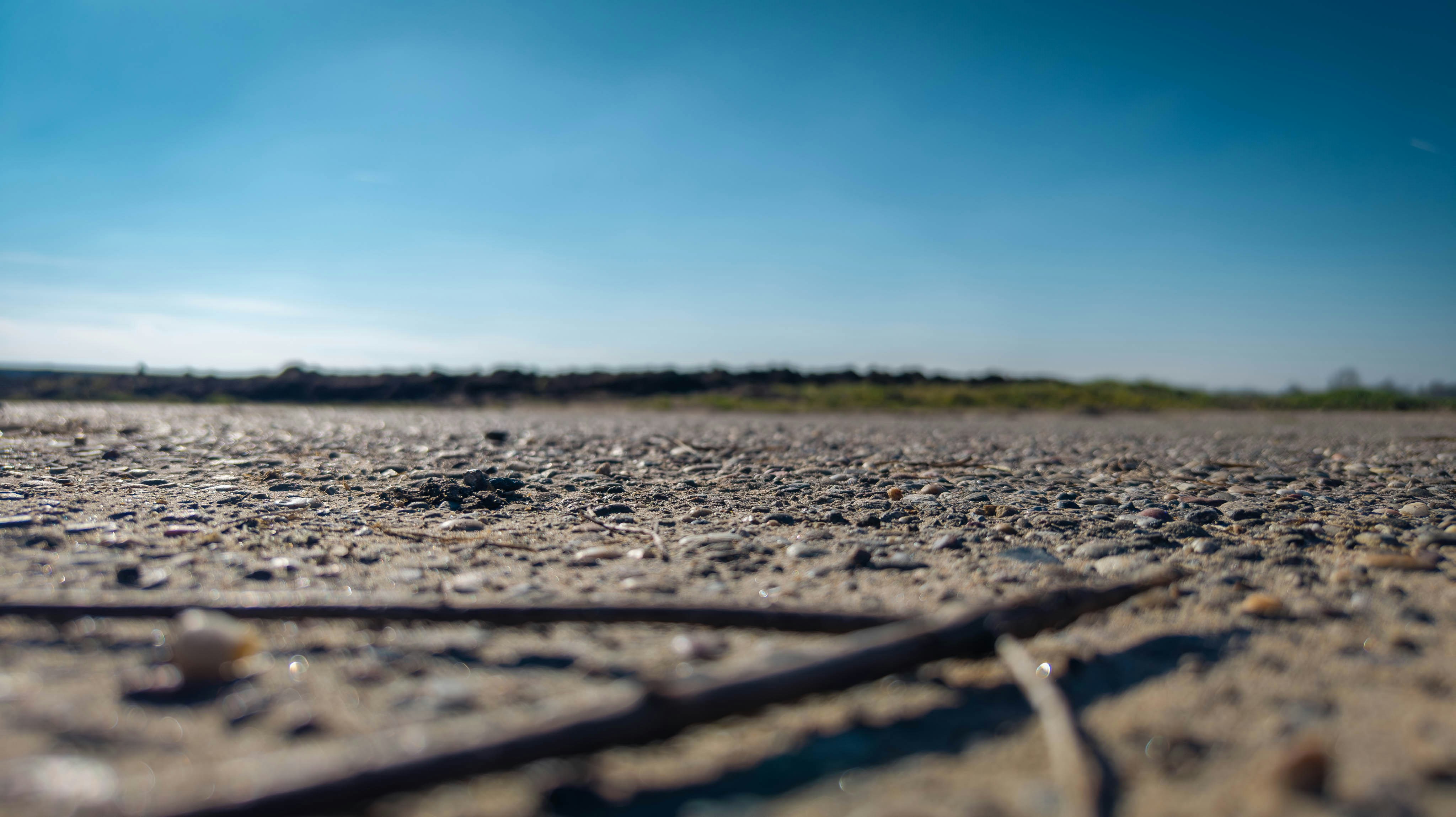 Low-angle view of a gravel path with small stones under a clear blue sky.