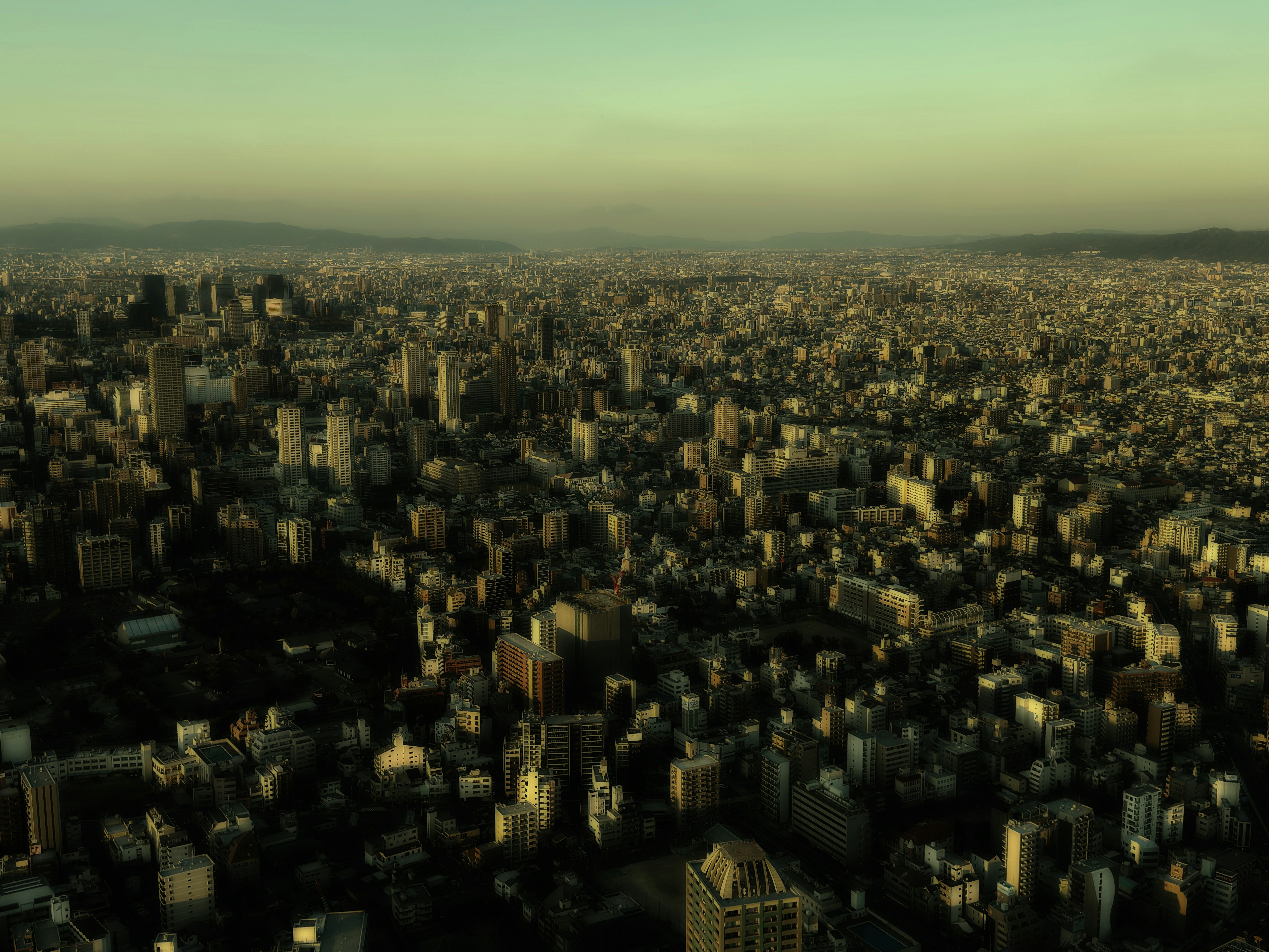 Dense cityscape under a soft sunrise glow with towering buildings casting long shadows.