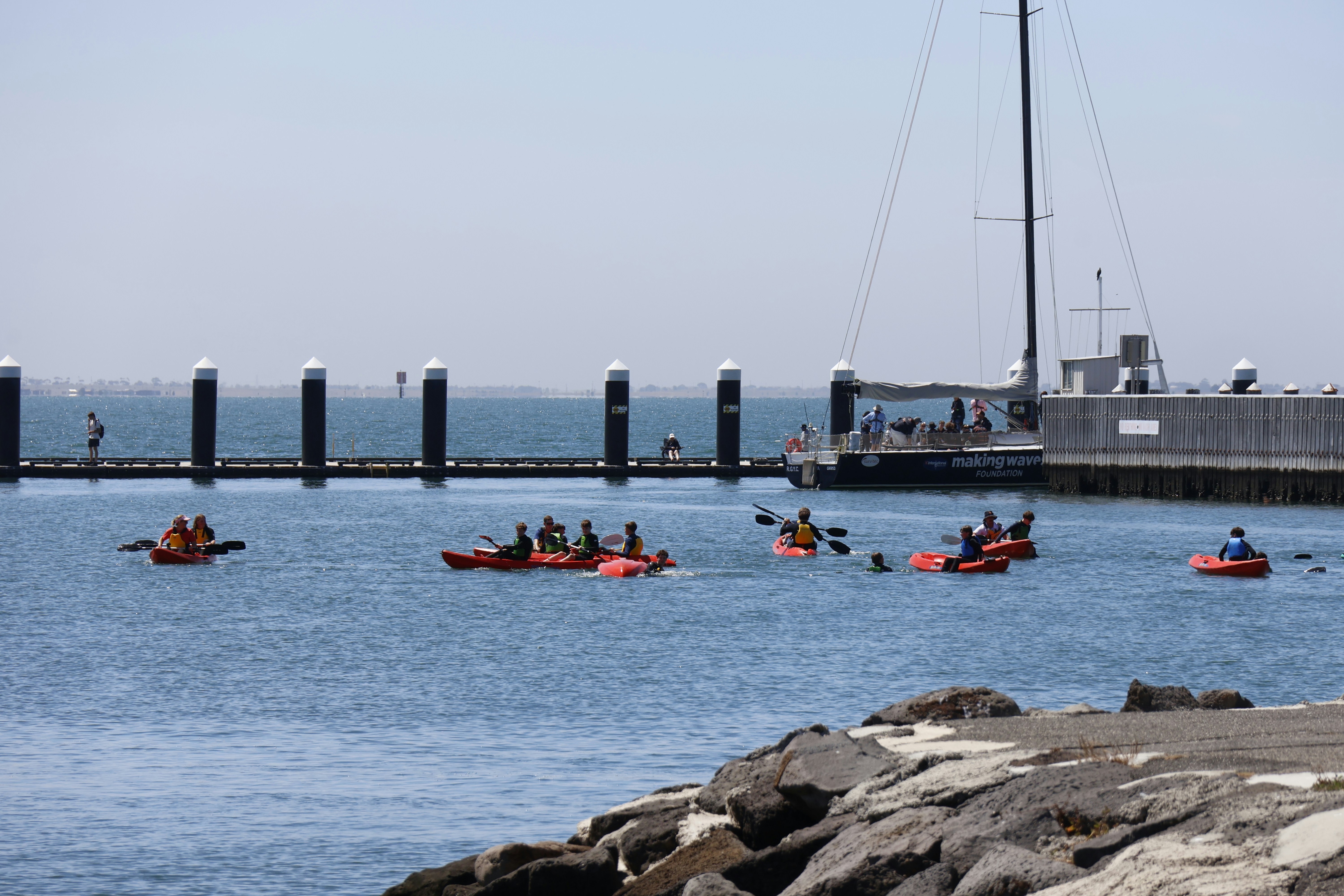 Kayakers paddle near a dock on a clear, sunny day.