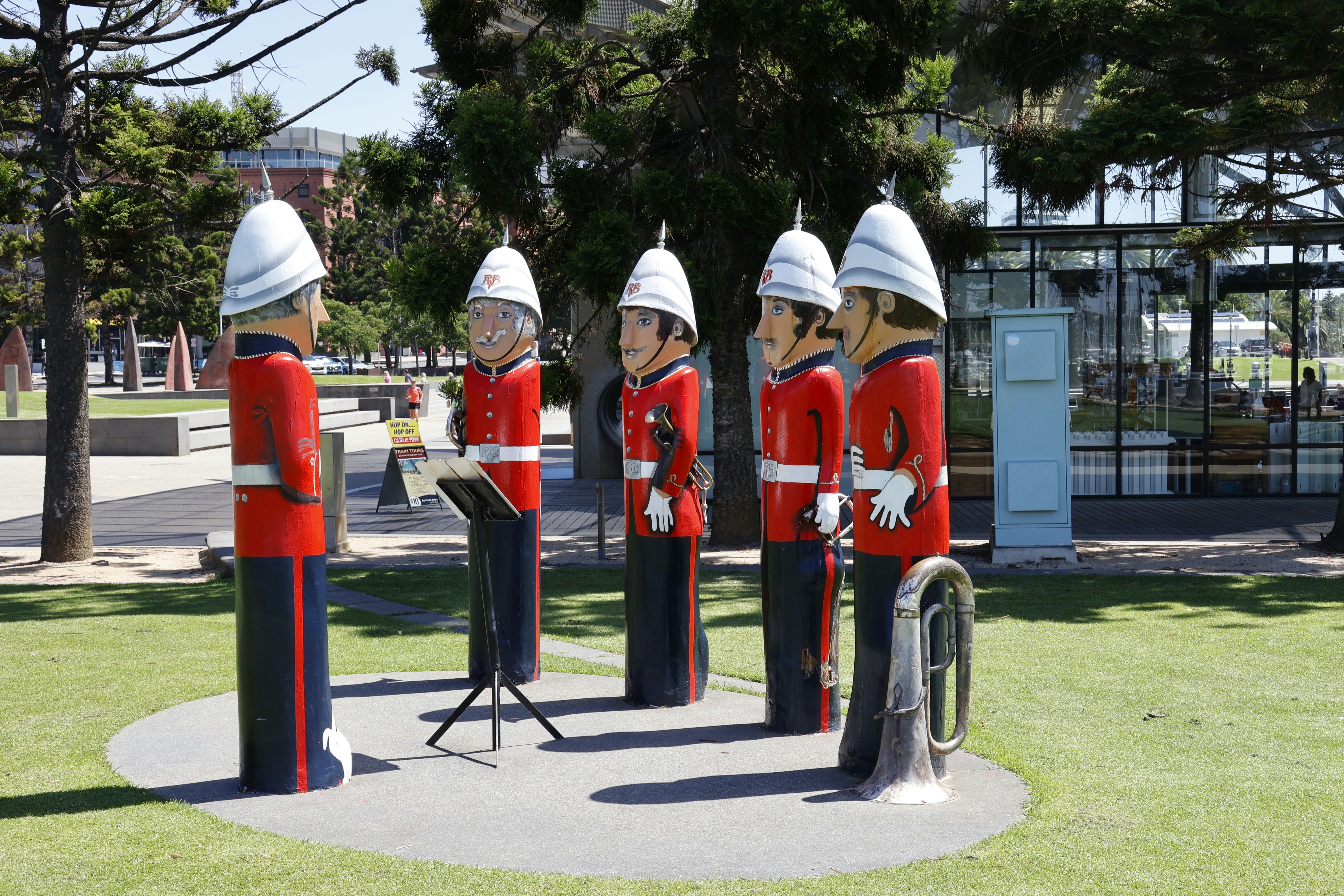 Colorful wooden statues of musicians dressed in red uniforms stand in a circle on a grassy lawn.
