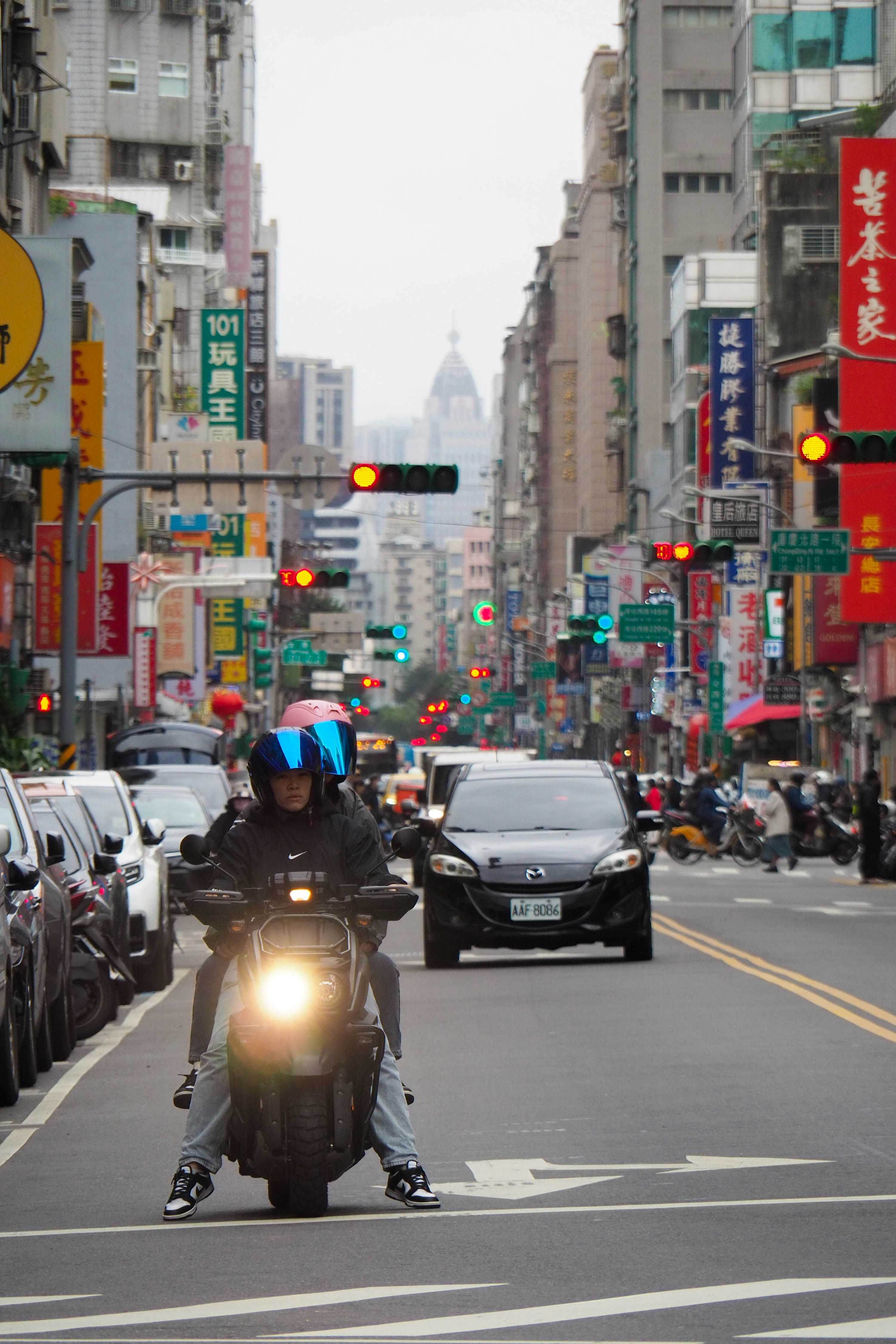 Motorcyclist with a bright headlight navigates a bustling city street lined with colorful signage and traffic.