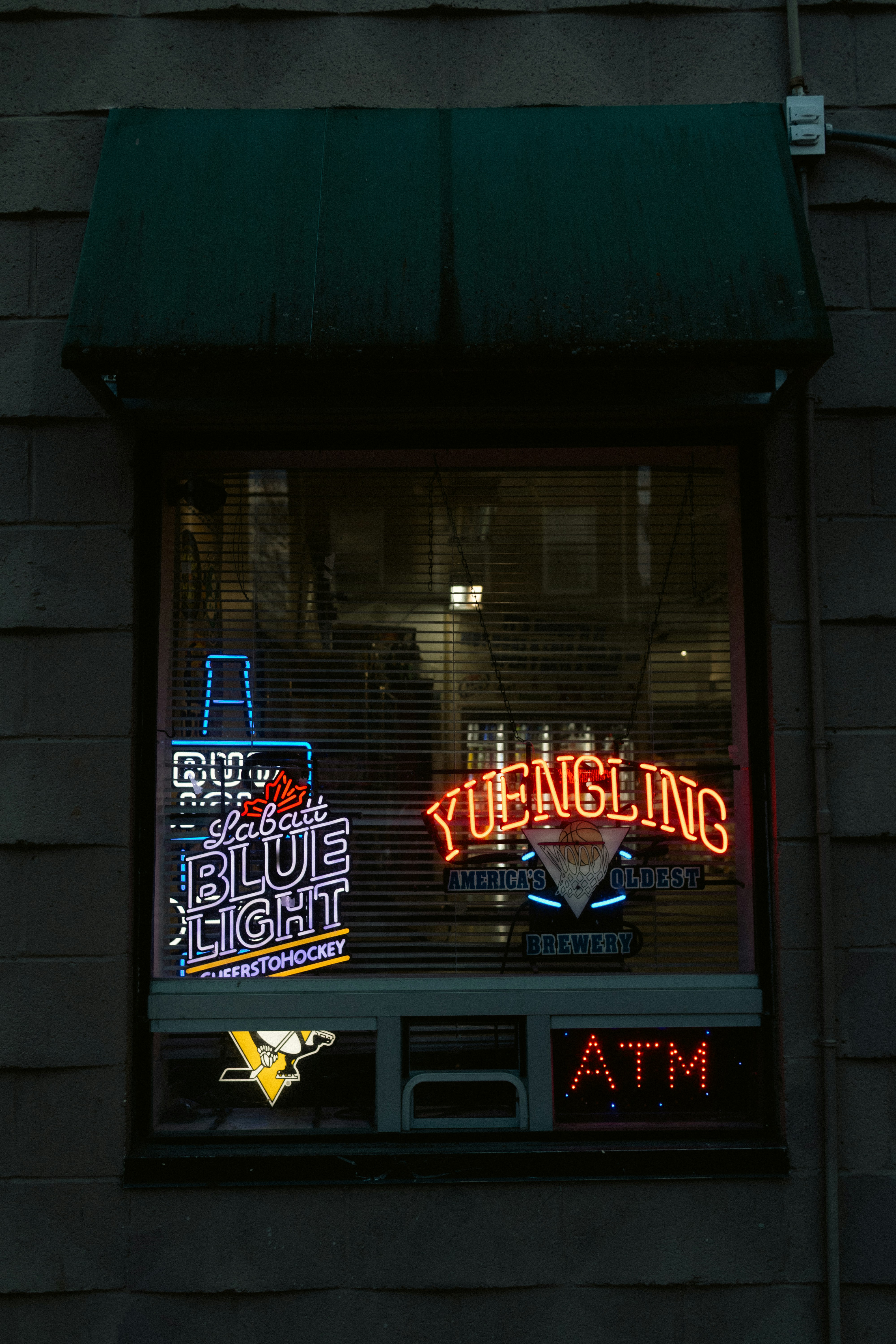 Neon signs illuminate a dimly lit window with advertisements for beer and an ATM.