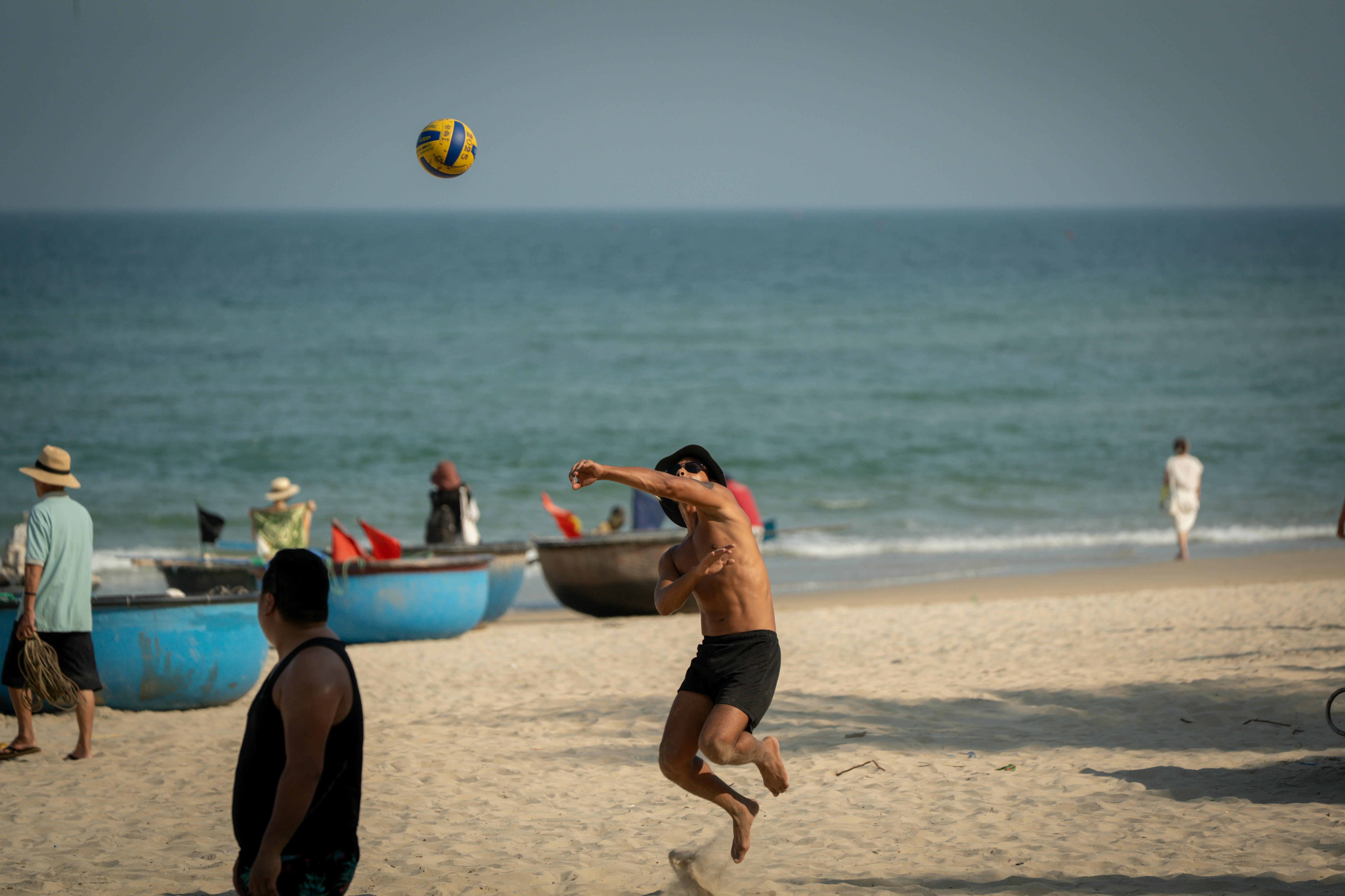 Airborne Volley at the Sunlit Beach: A Jumping Player Among Boats and Sea