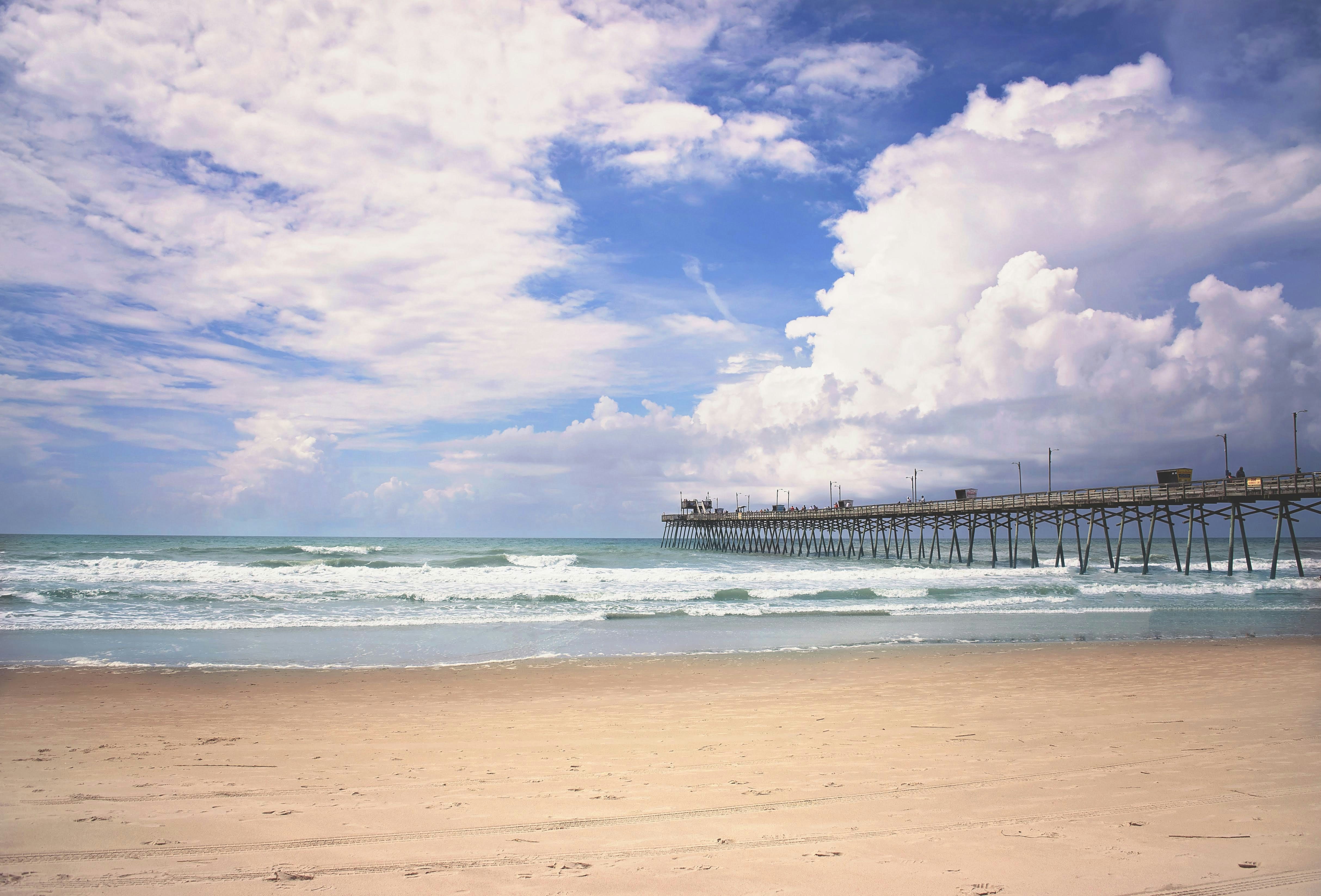 Beach scene with waves, pier, and cloudy sky. photo – Free Beach Image ...
