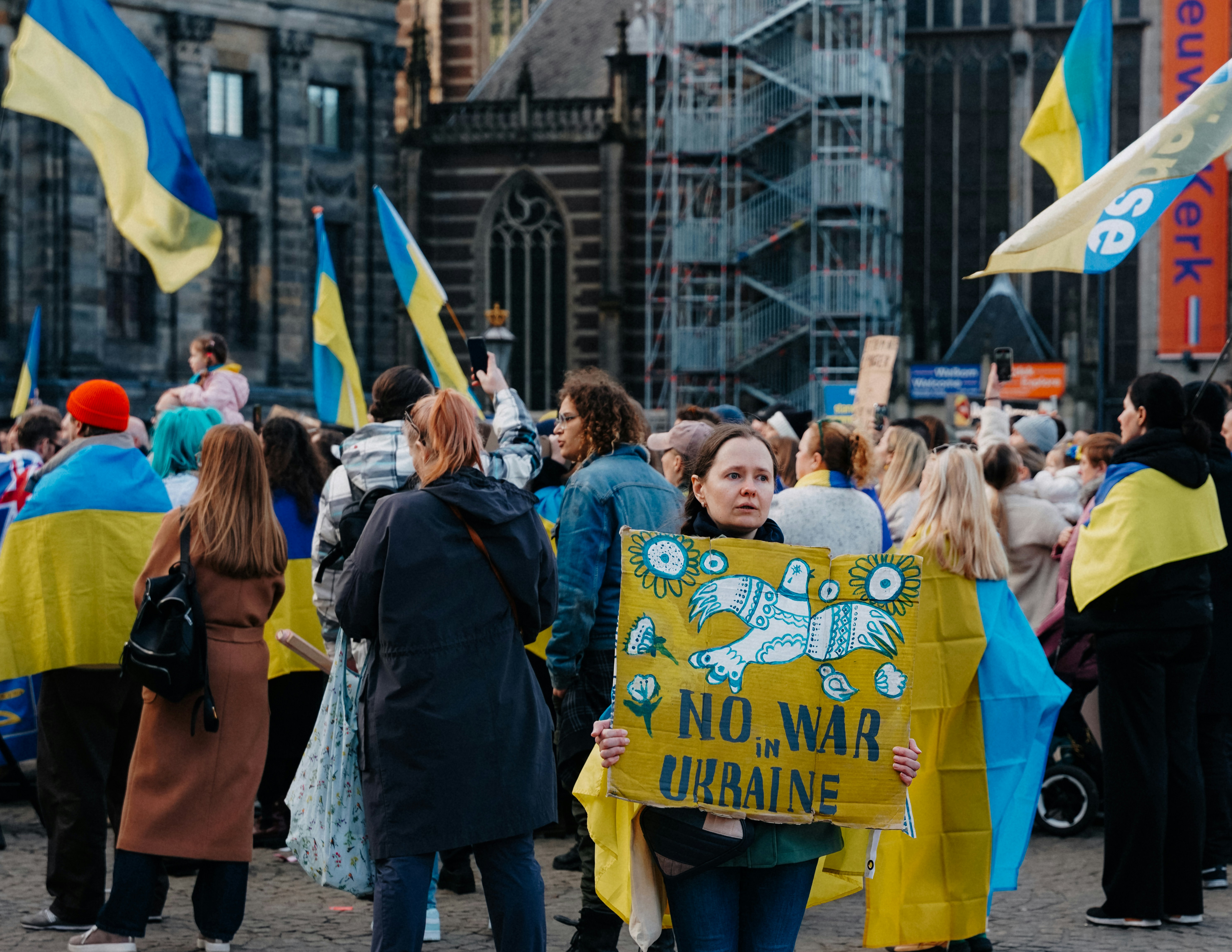 Crowd gathered with Ukrainian flags and anti-war signs in an urban setting.