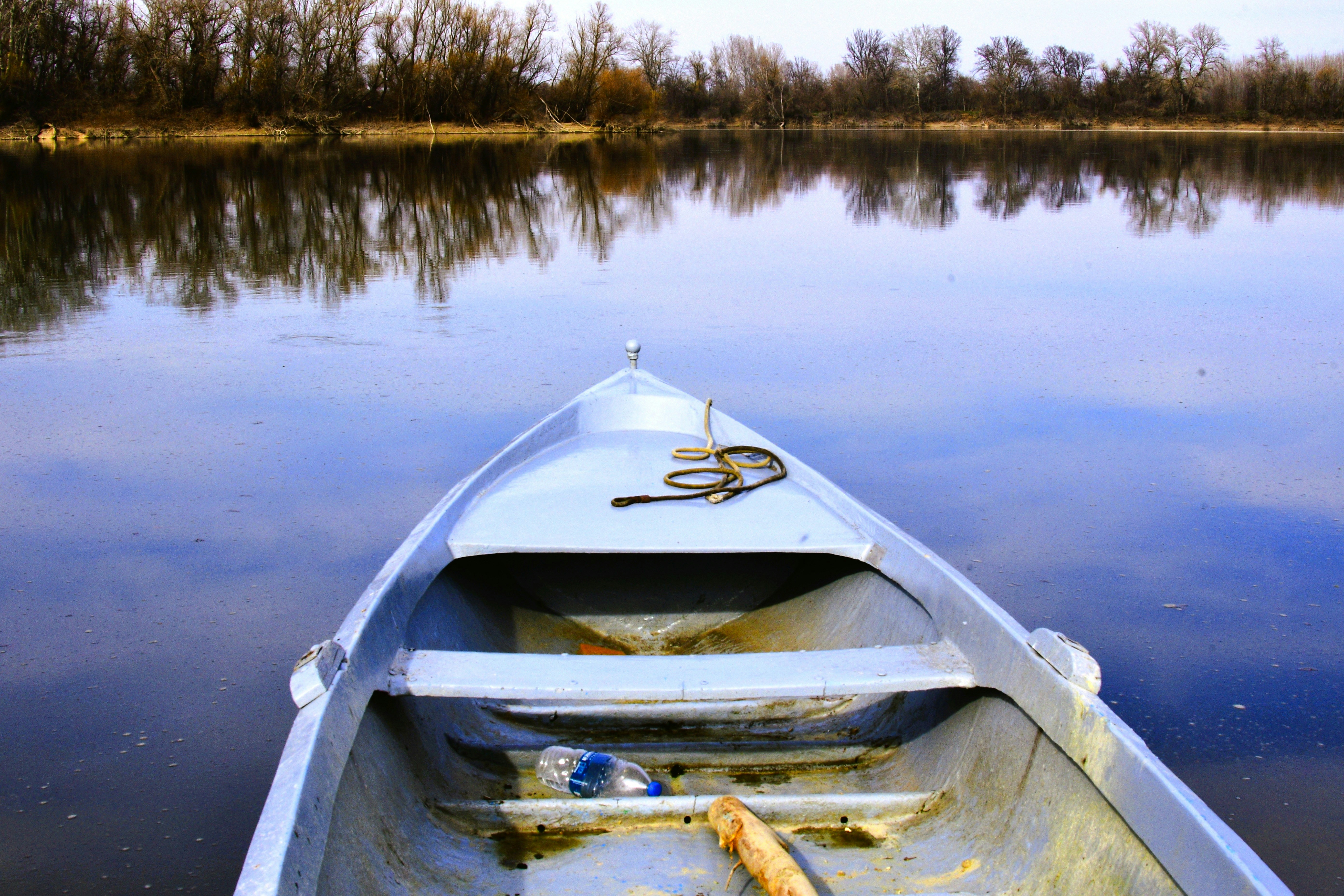 Weathered boat resting on calm waters, surrounded by trees reflecting in the water's surface.