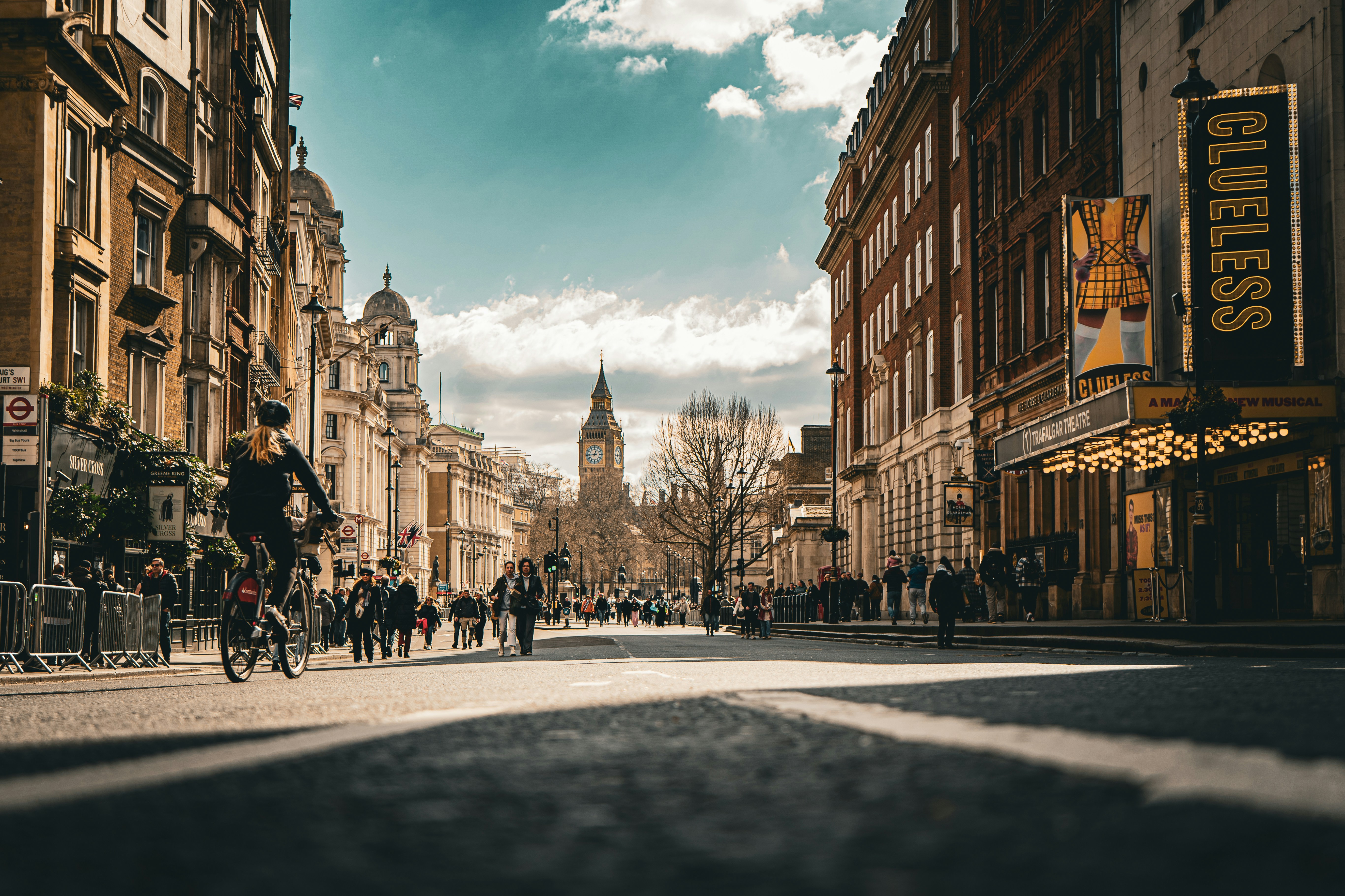 Cyclist and pedestrians on a bustling city street with historic architecture and a theater marquee under a bright sky.