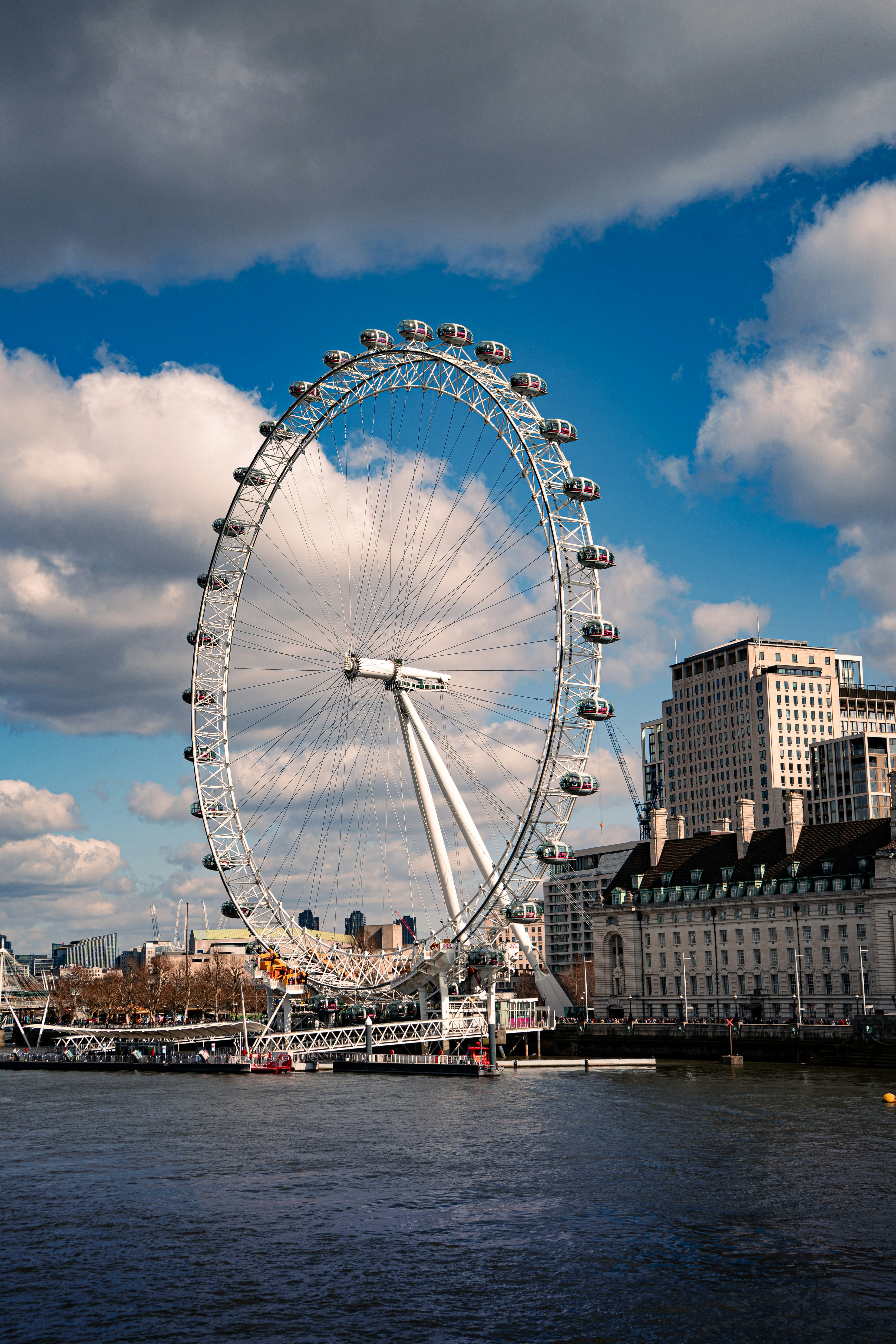London Eye towering over the River Thames, framed by a backdrop of dramatic clouds and urban architecture.