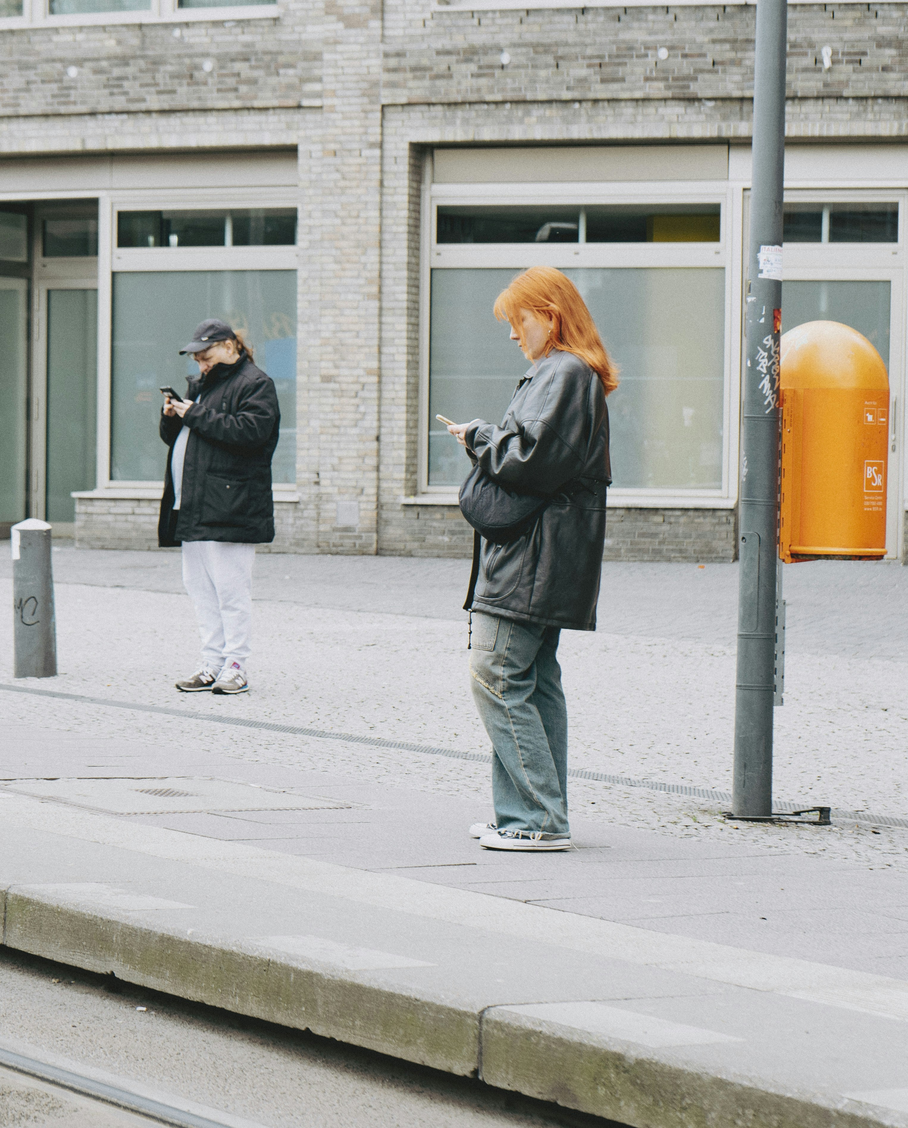 Orange Hair, Quiet Street: A Phone Pause on the Sidewalk