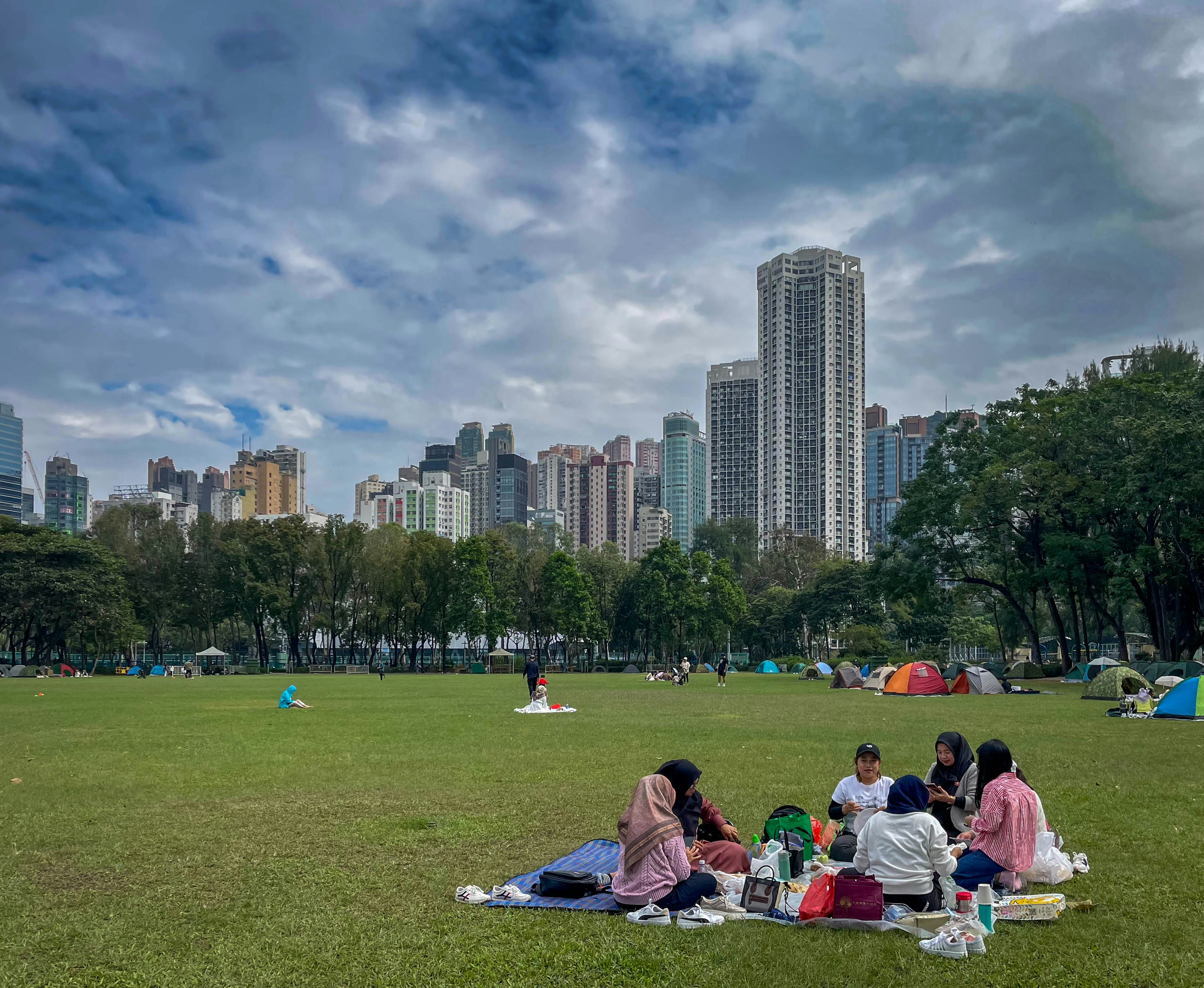 Group enjoying a picnic in a park with colorful tents and skyscrapers in the background.