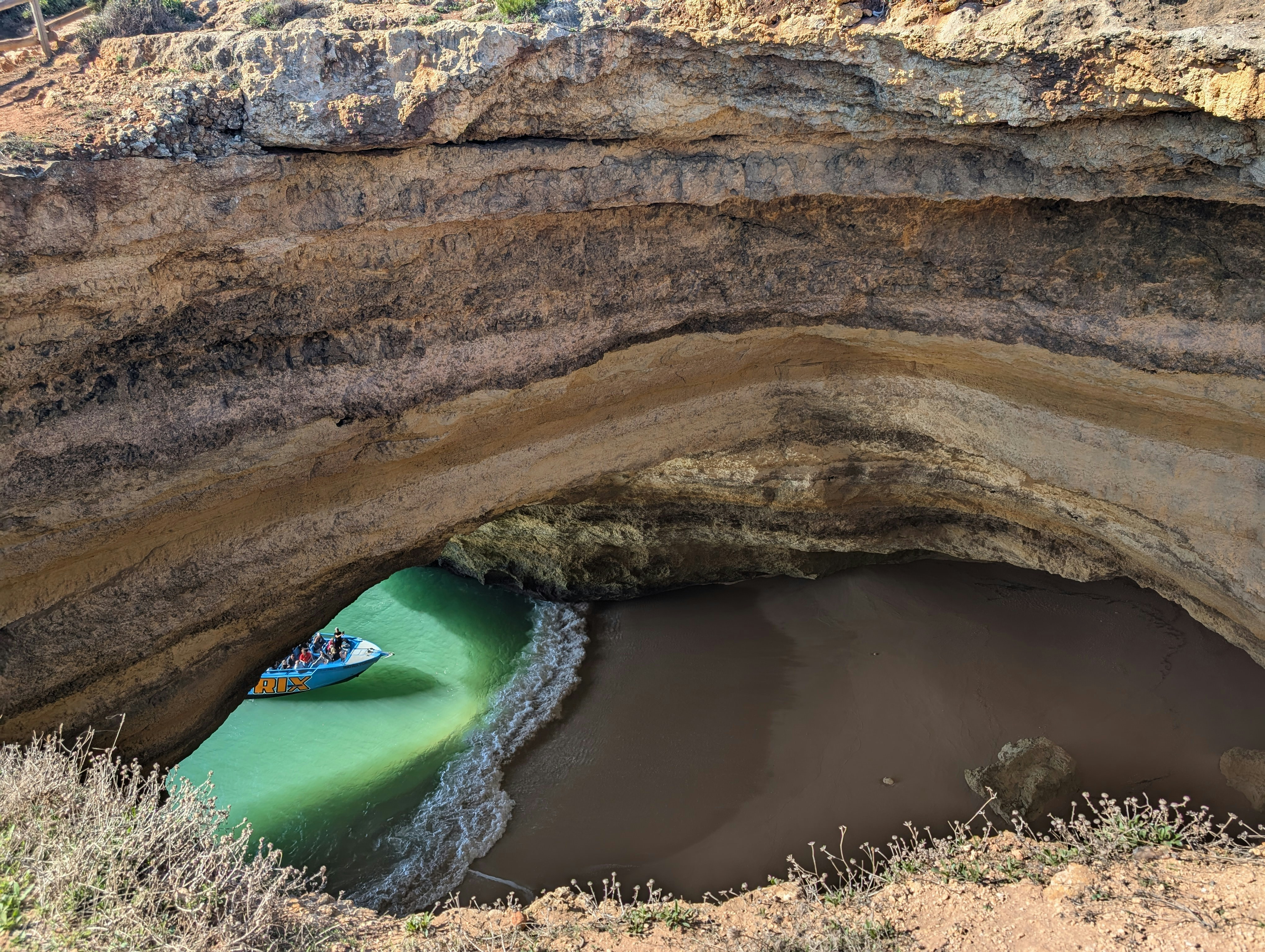 Boat anchored in a turquoise cove beneath a natural rock archway.