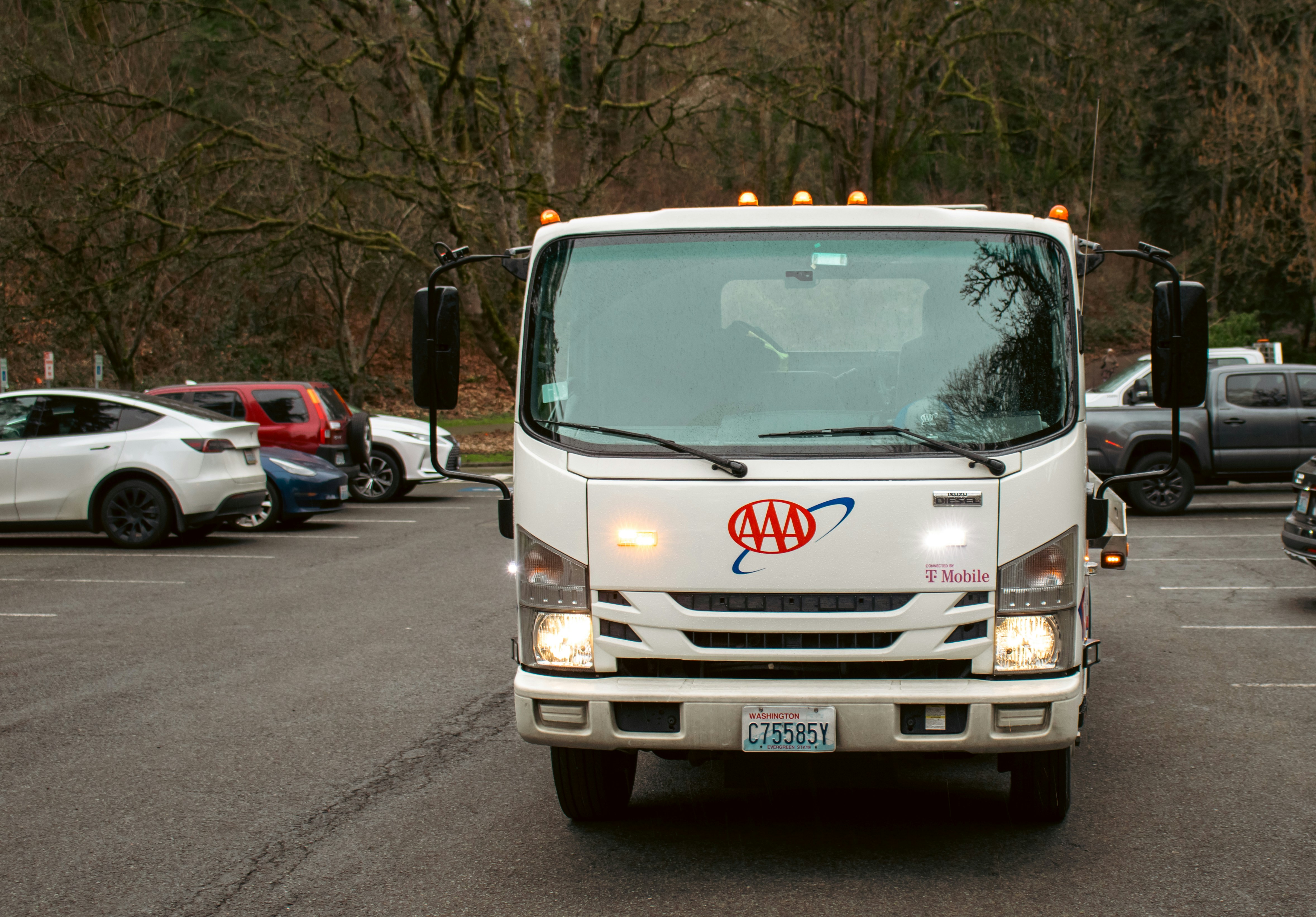 White AAA tow truck parked on a wet road surrounded by trees and cars.