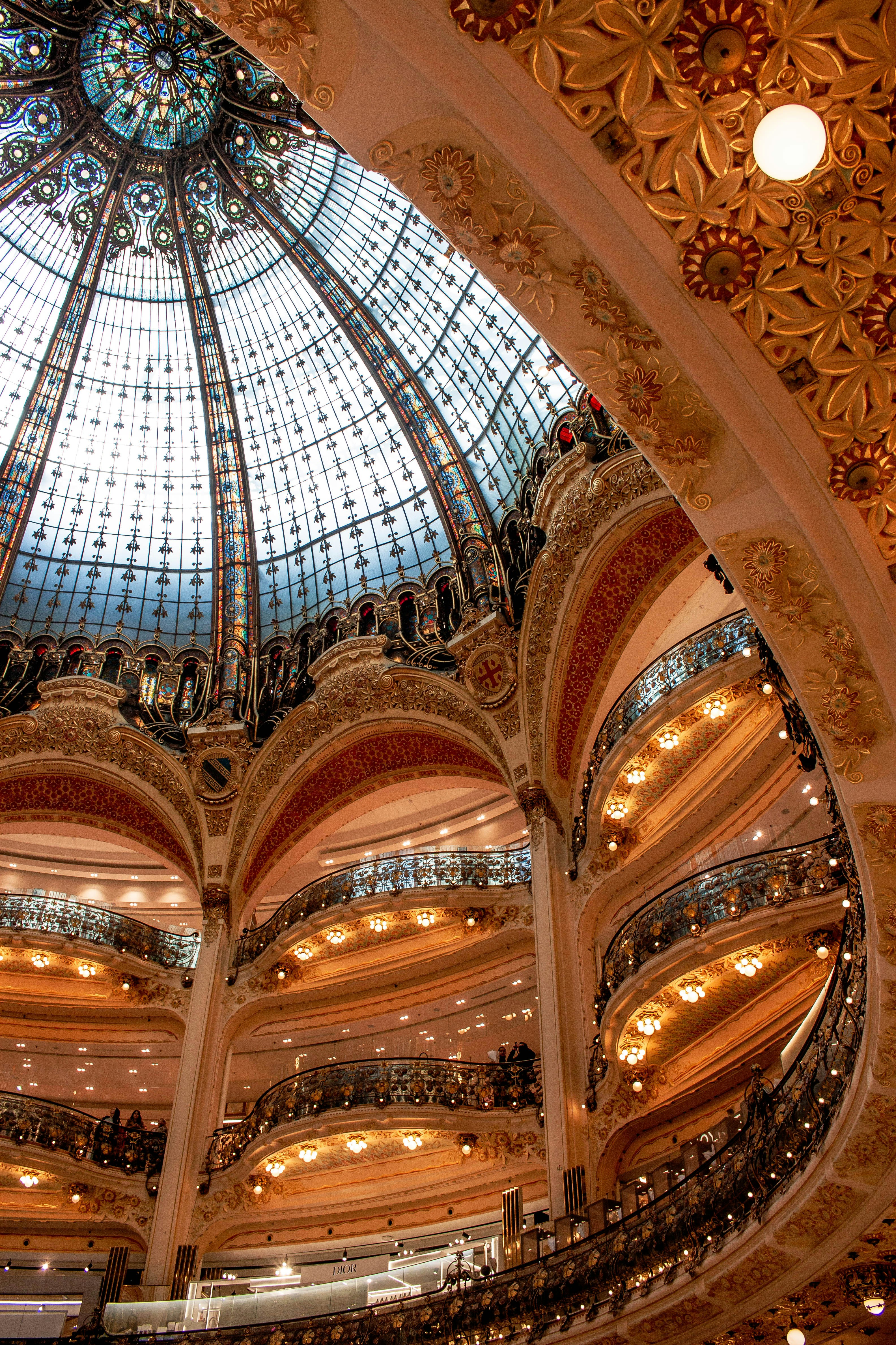 Grand interior of a multi-tiered building with a magnificent stained-glass dome and ornate decorations.