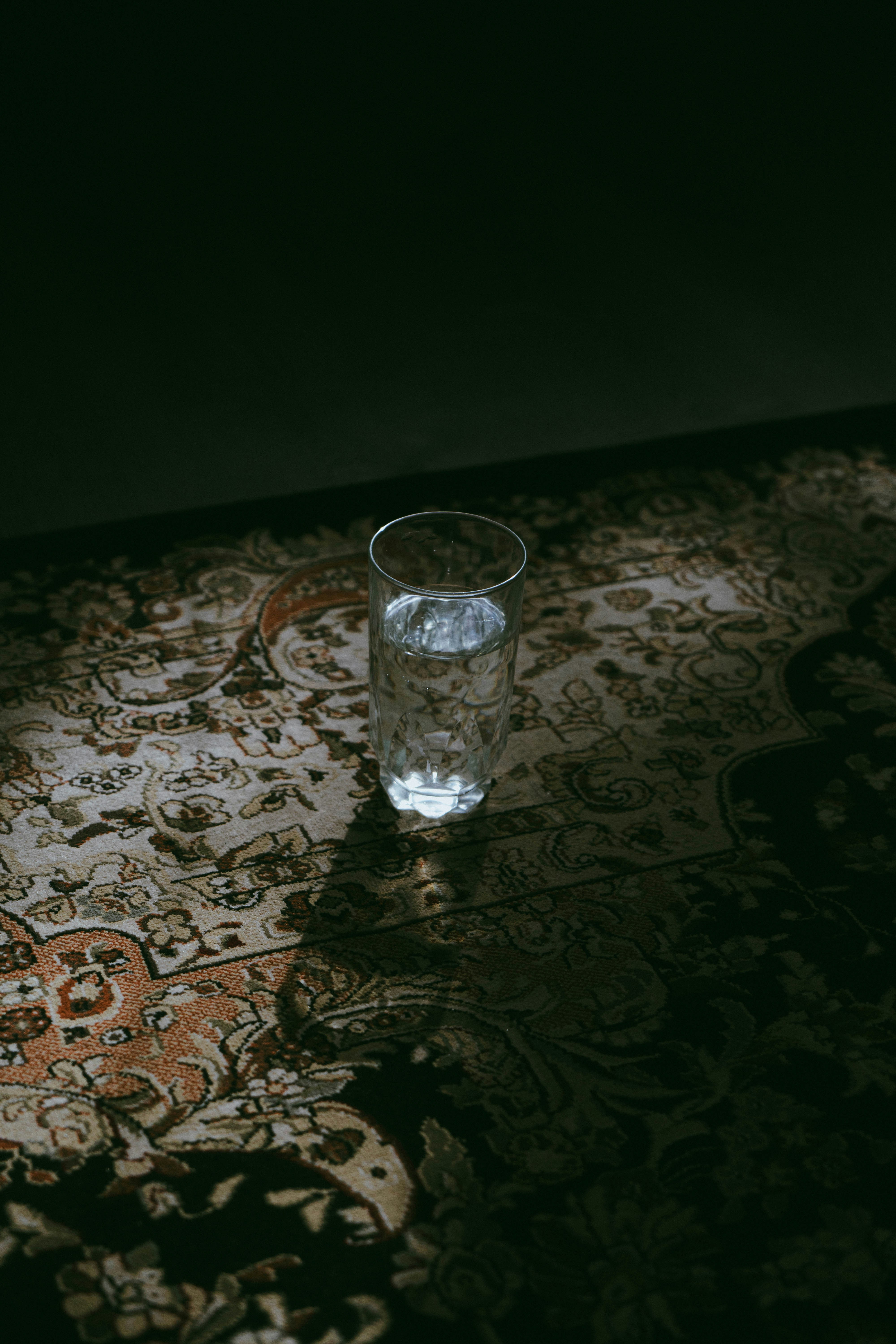 Solitary Glass Under a Narrow Spotlight on an Ornate Rug