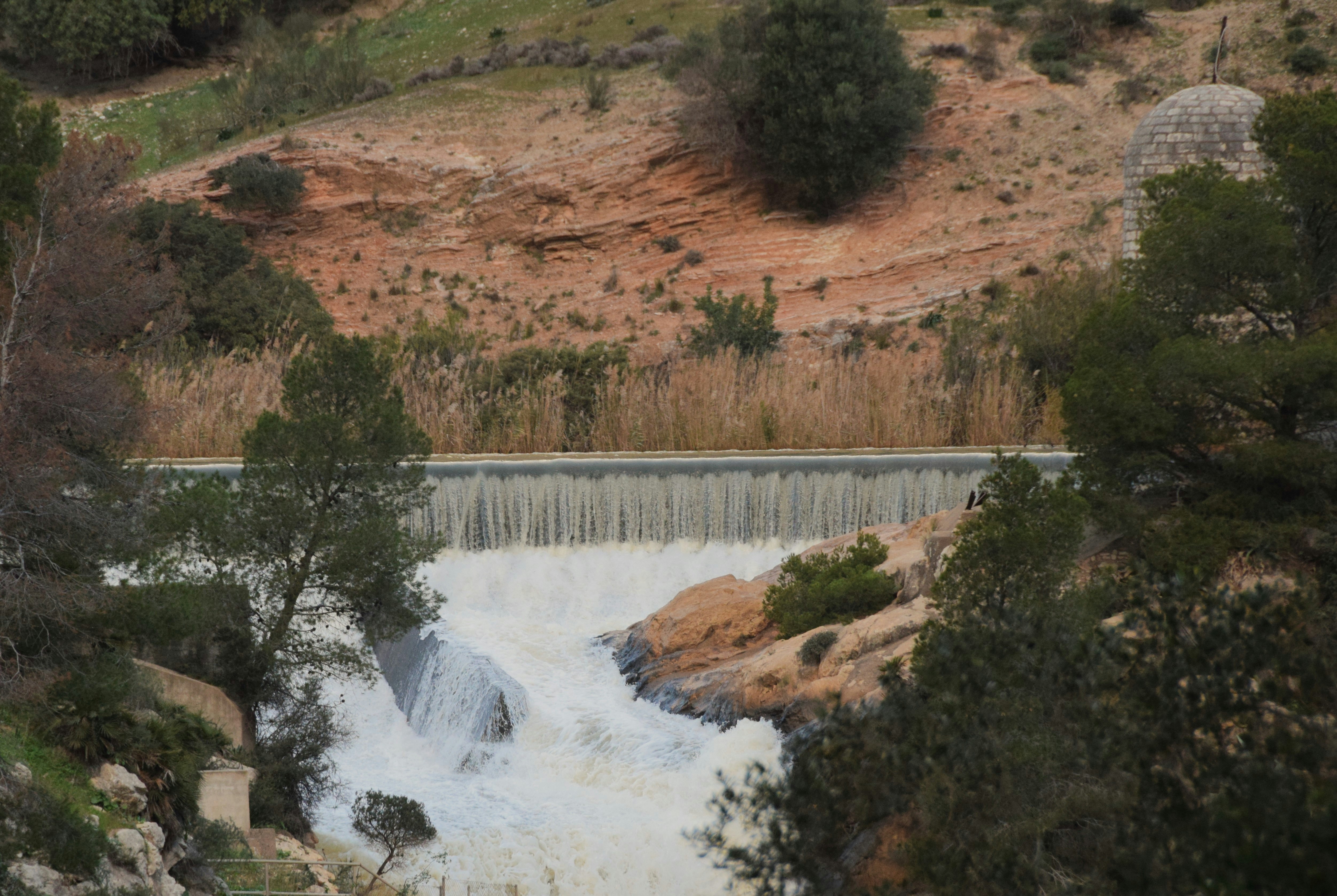 Waterfall cascading over rocks in a lush, hilly landscape.