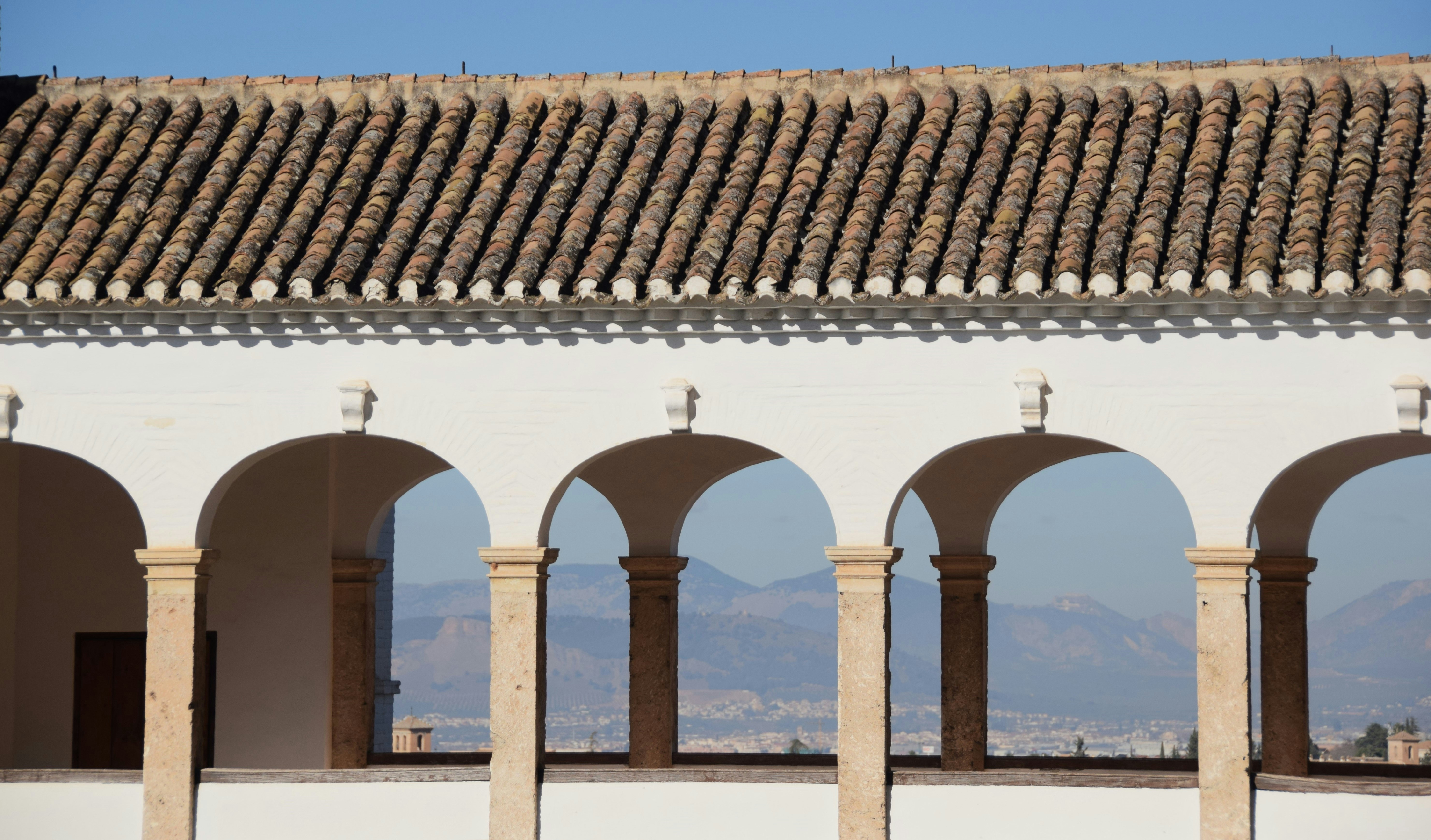 Colonnade with a tiled roof, arches framing distant mountains under a clear blue sky.
