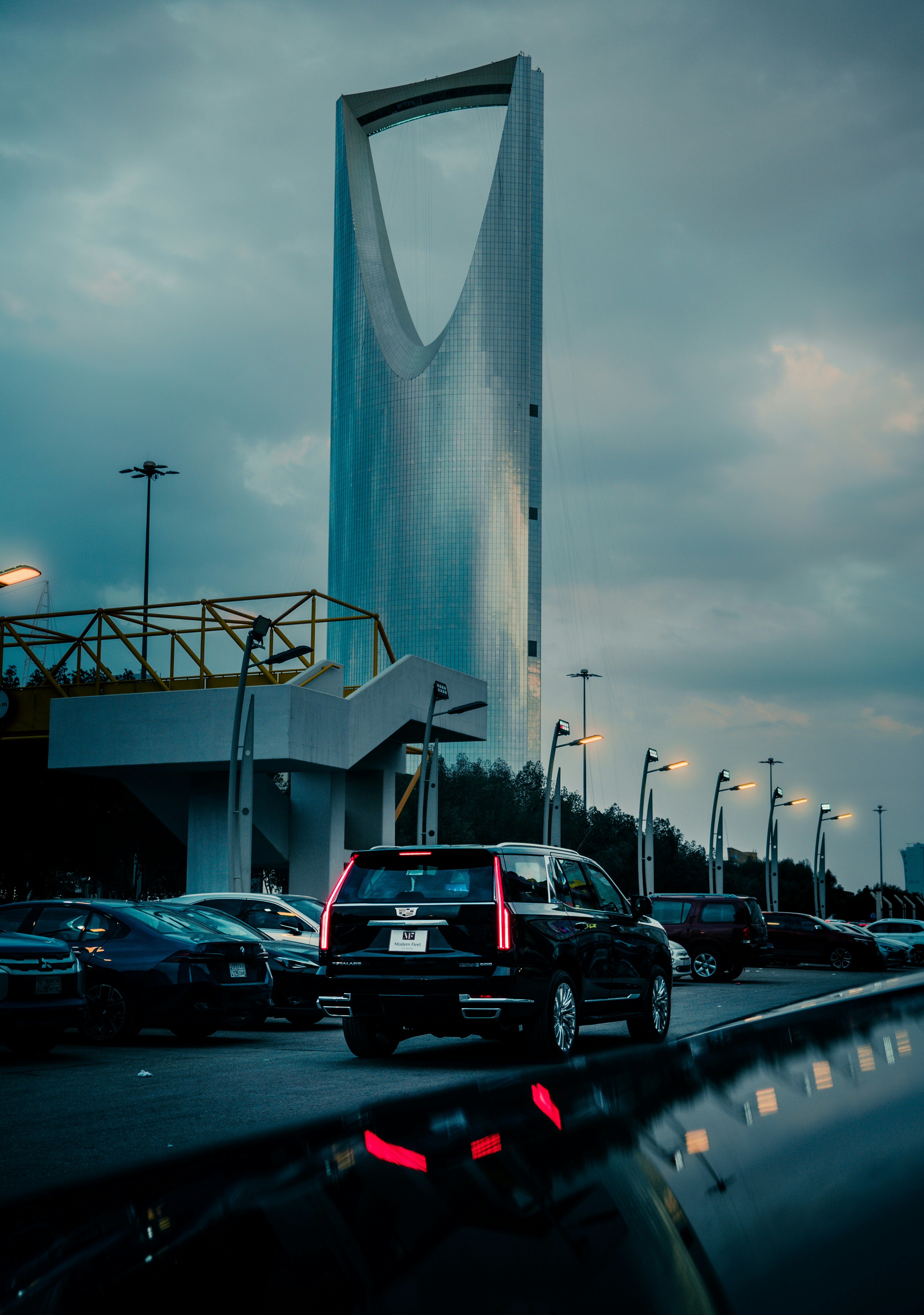 A sleek black SUV parked in a lot, with a modern skyscraper reflecting the evening sky in the background. The scene captures the essence of urban architecture and contemporary lifestyle.