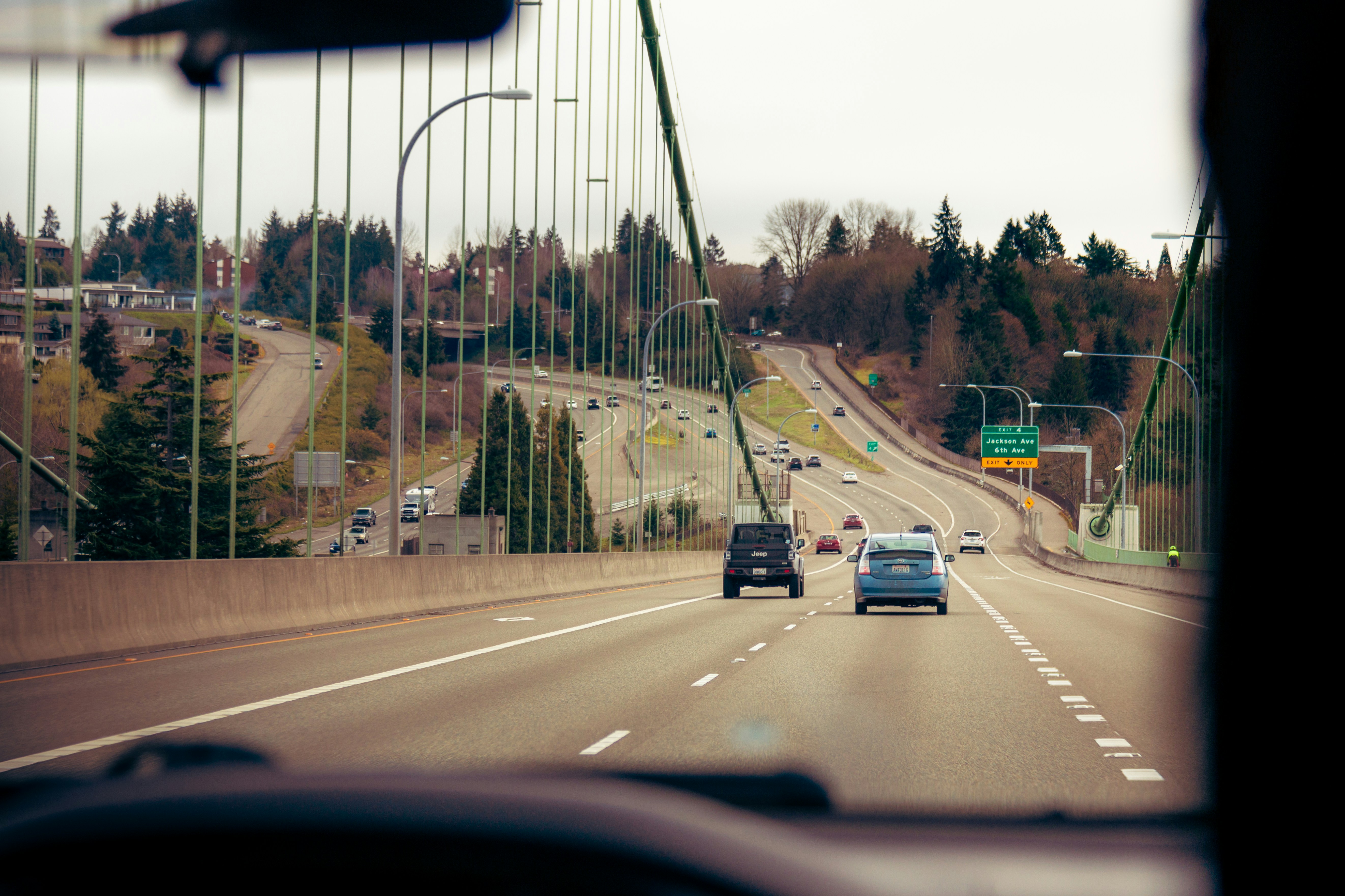 View from a car interior driving over a bridge with distant trees and urban landscape.