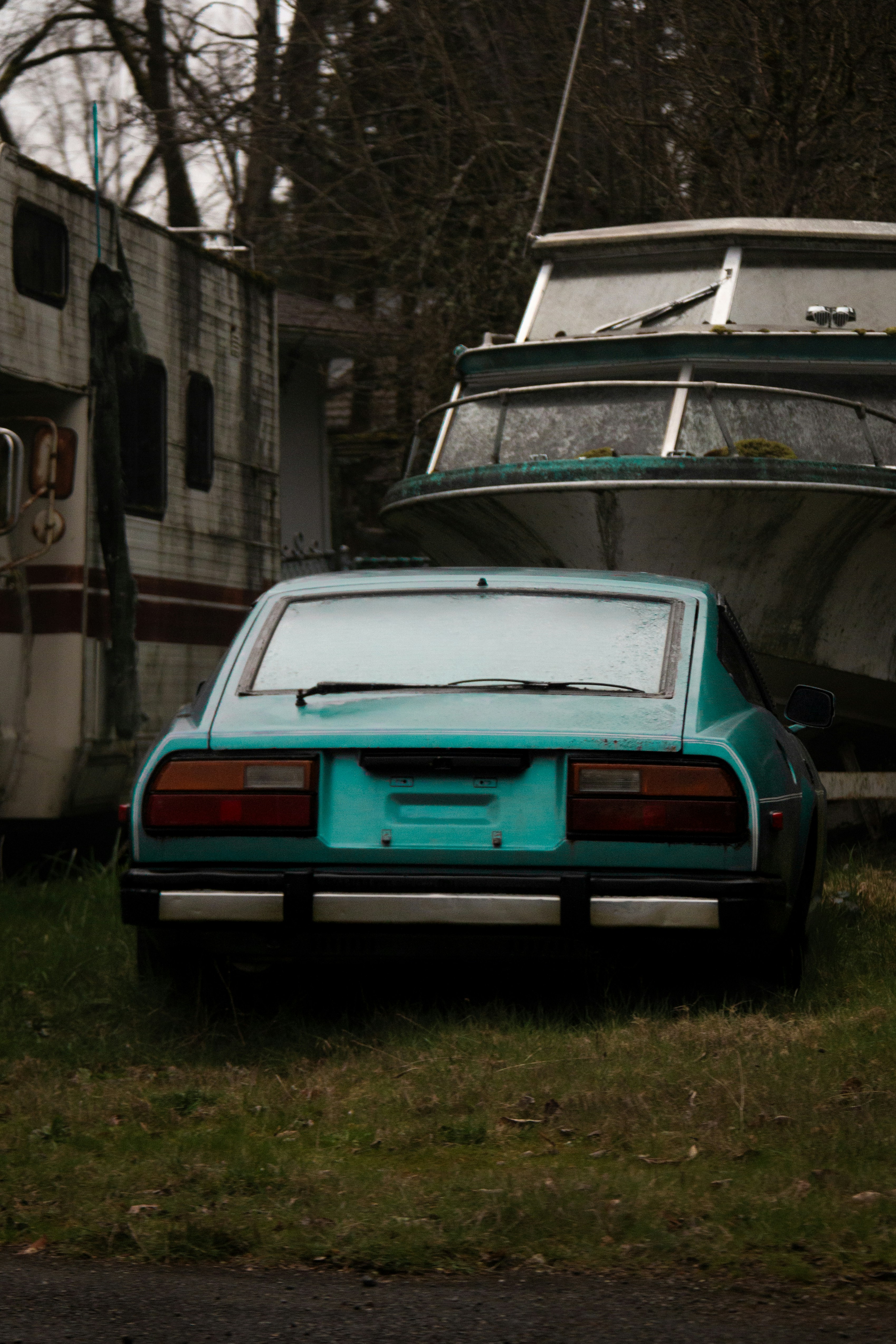 An old car without a license plate sitting in front of an old boat