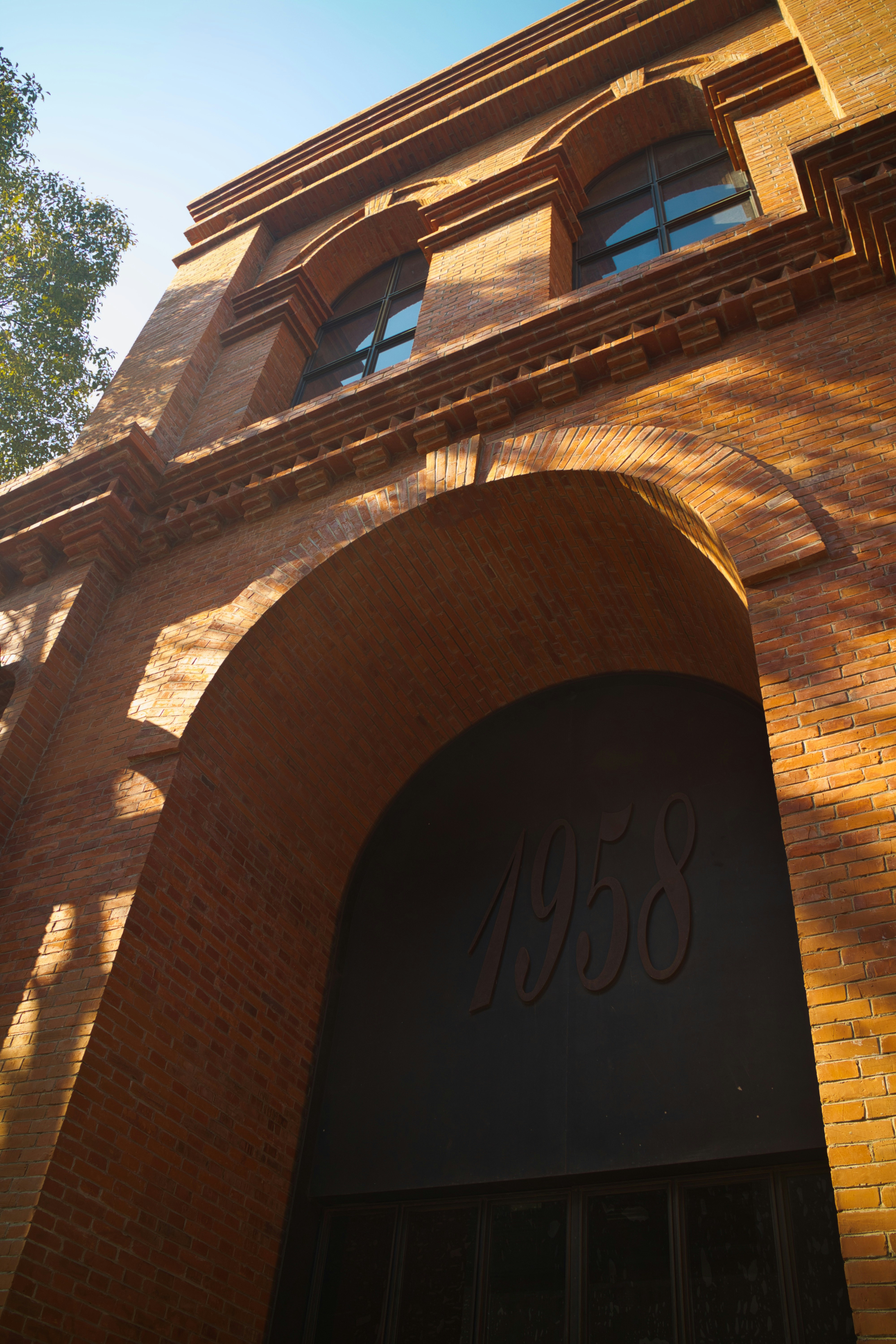 1958 Archway: Sunlit Brick Portal Under Historic Windows