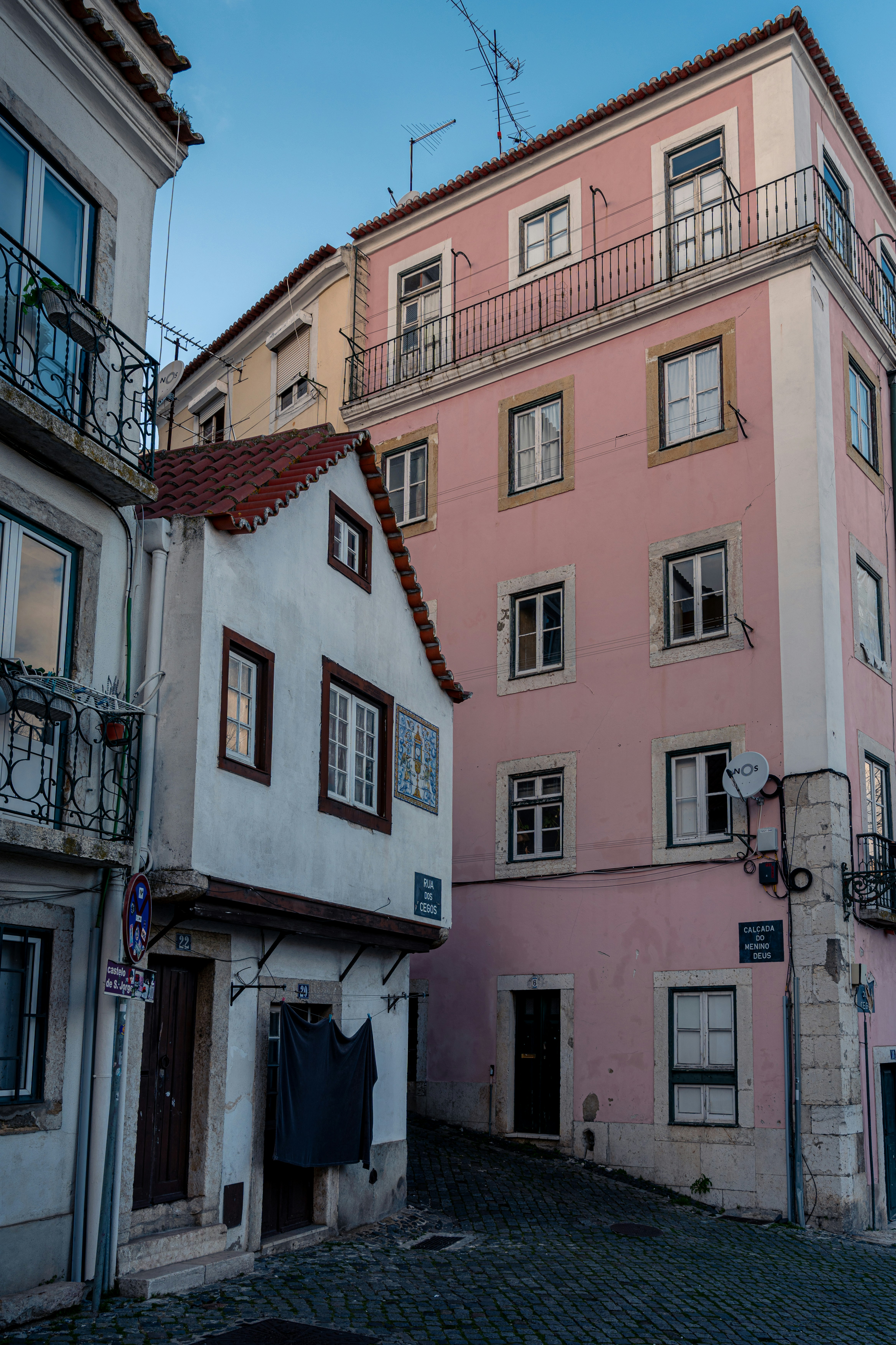 Narrow cobblestone street flanked by houses with pastel-colored walls and traditional windows under a clear sky.