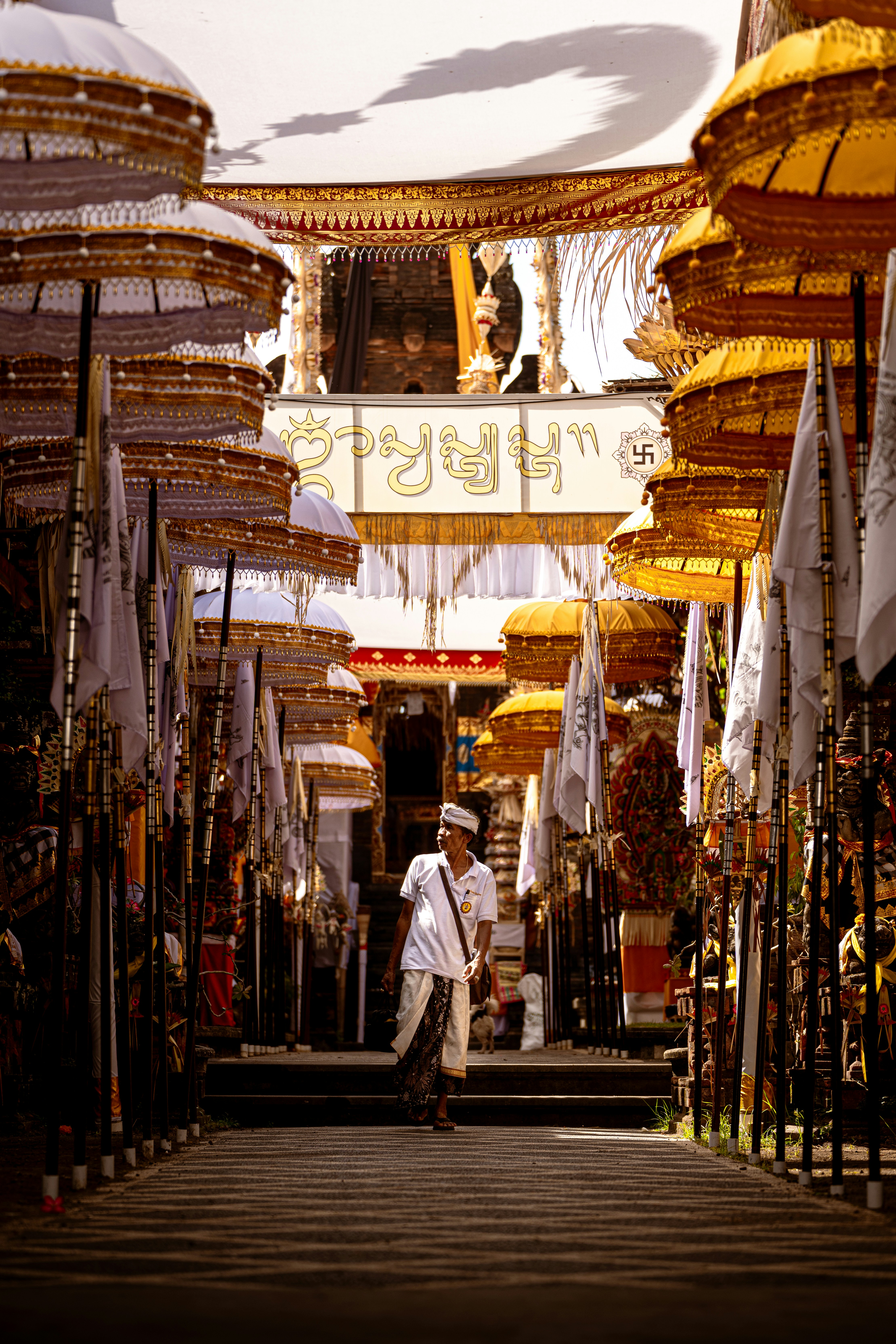 Person walking amidst rows of decorative umbrellas and flags in a sunlit courtyard.