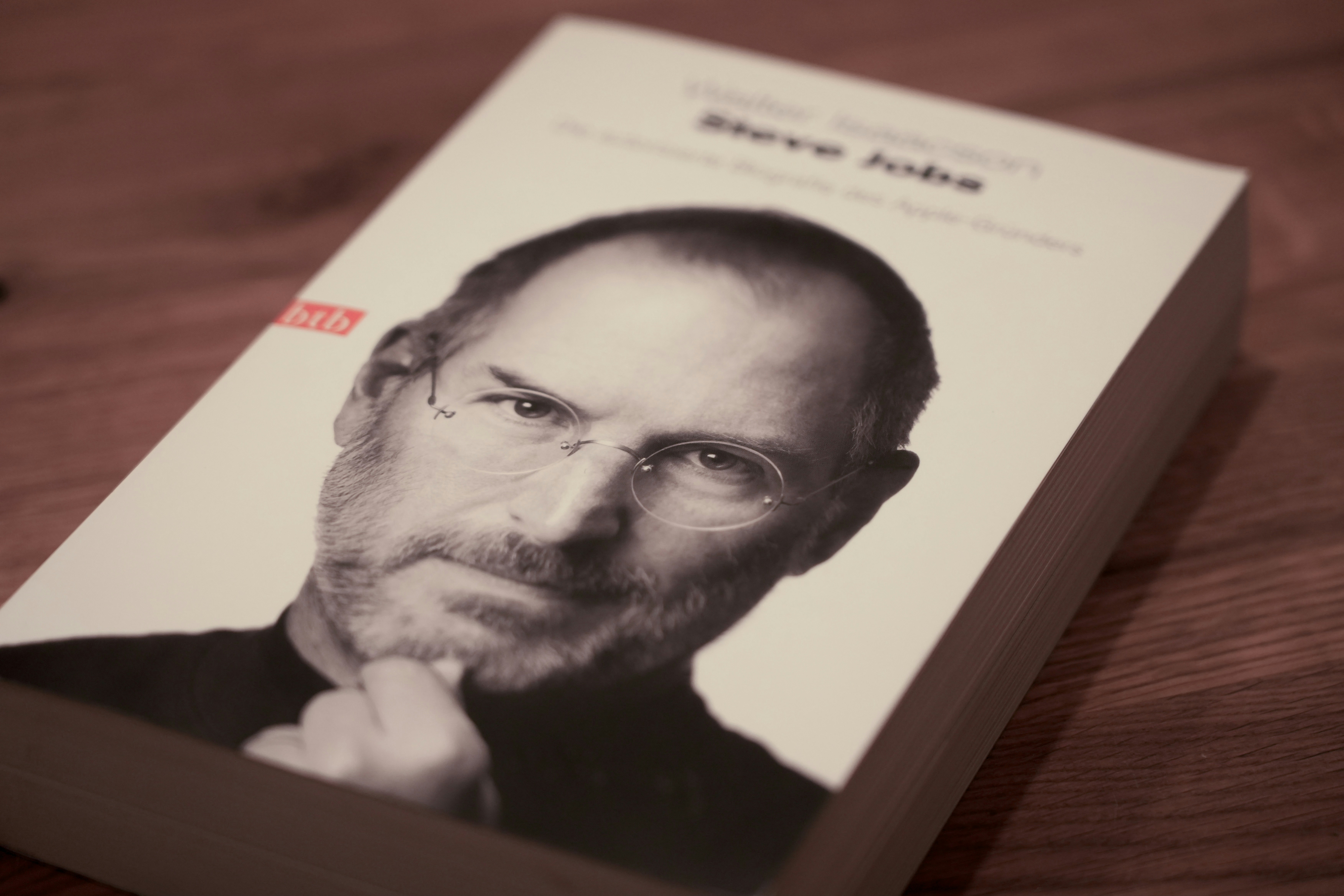 Biography of Steve Jobs with a black and white portrait cover on a wooden surface.