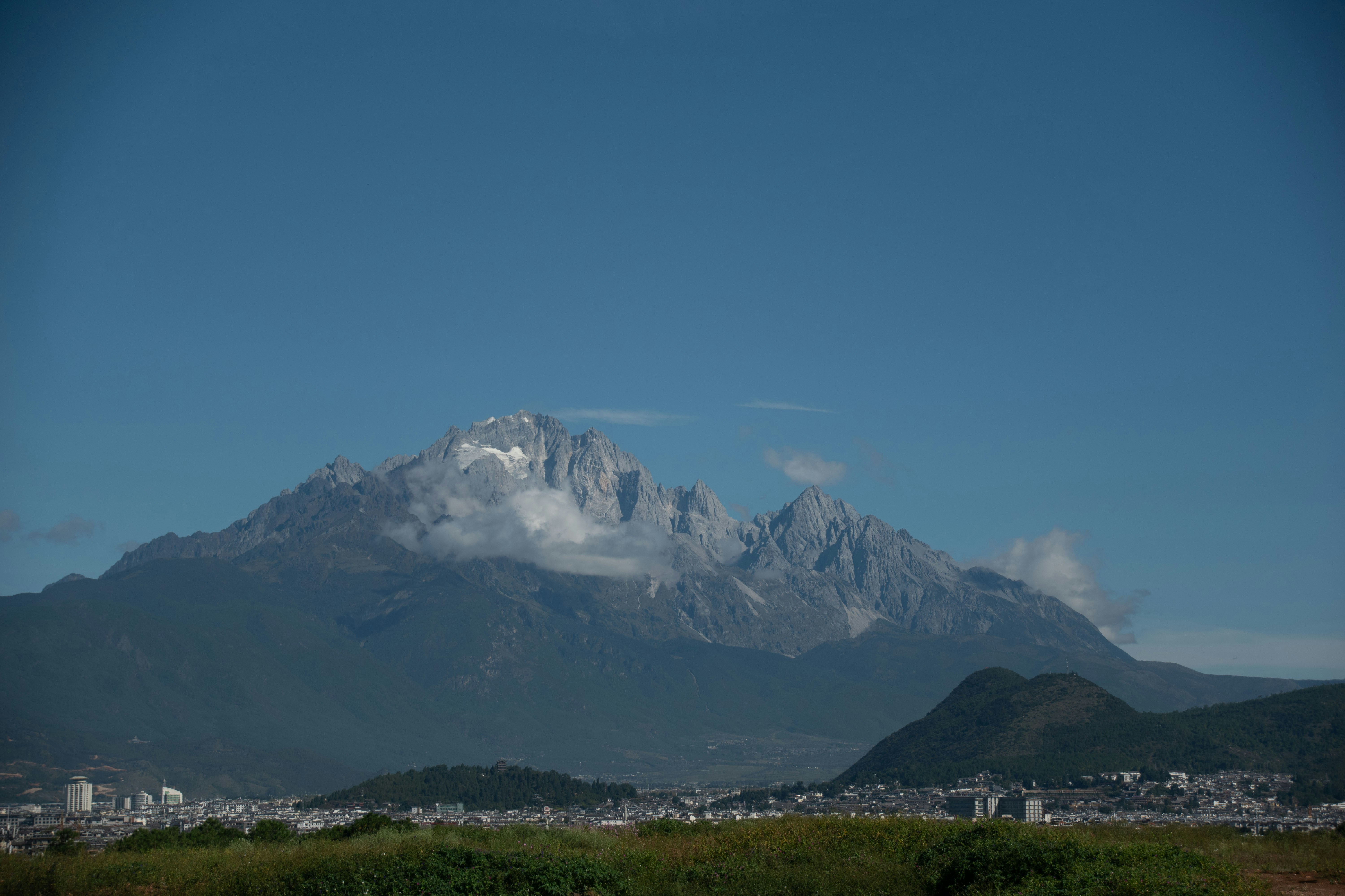 Snow-capped mountain range rises dramatically against a clear blue sky, with a cityscape visible in the foreground.