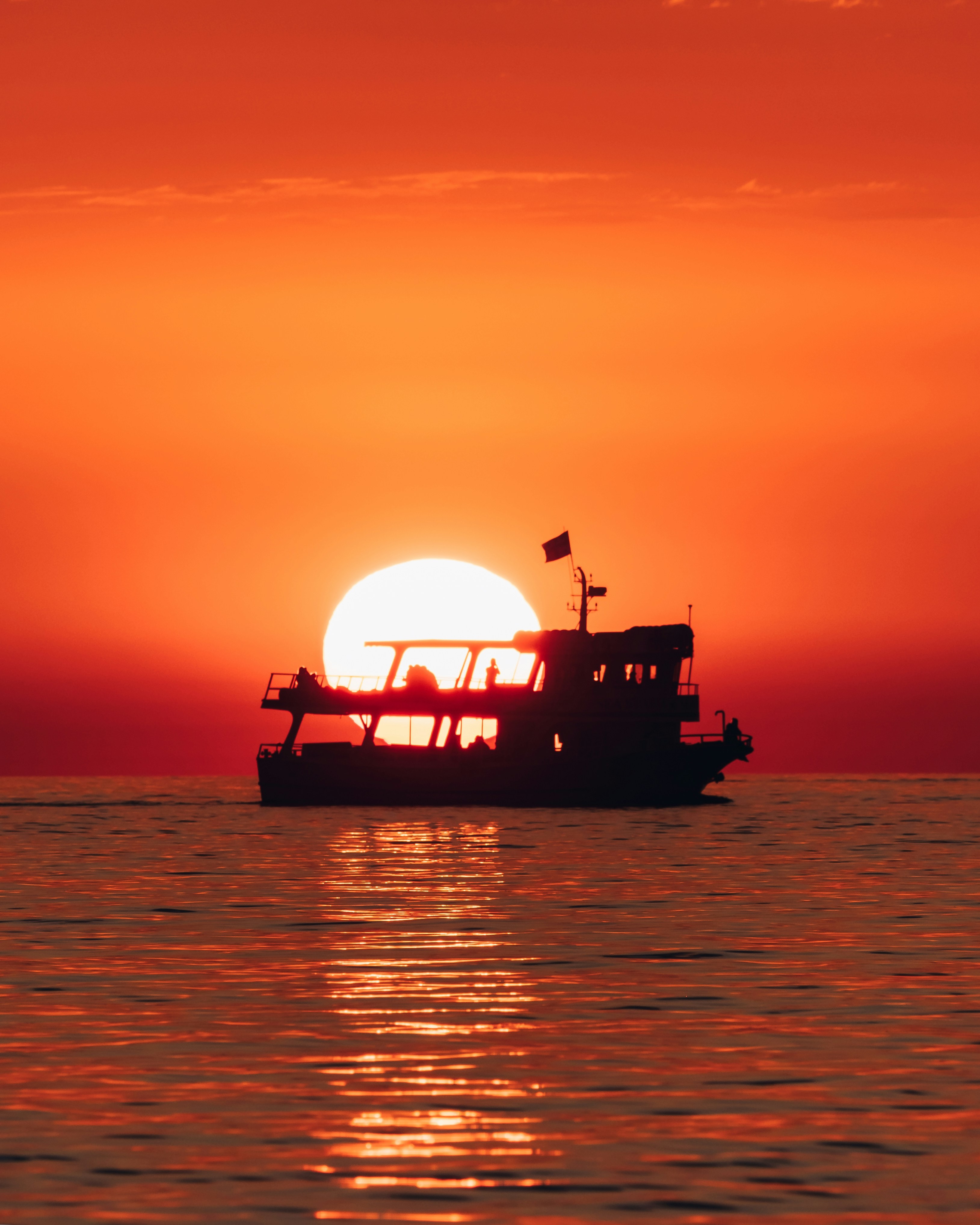 Horizon Silhouette: A Two-Deck Boat Drifts Under a Coral Sunset