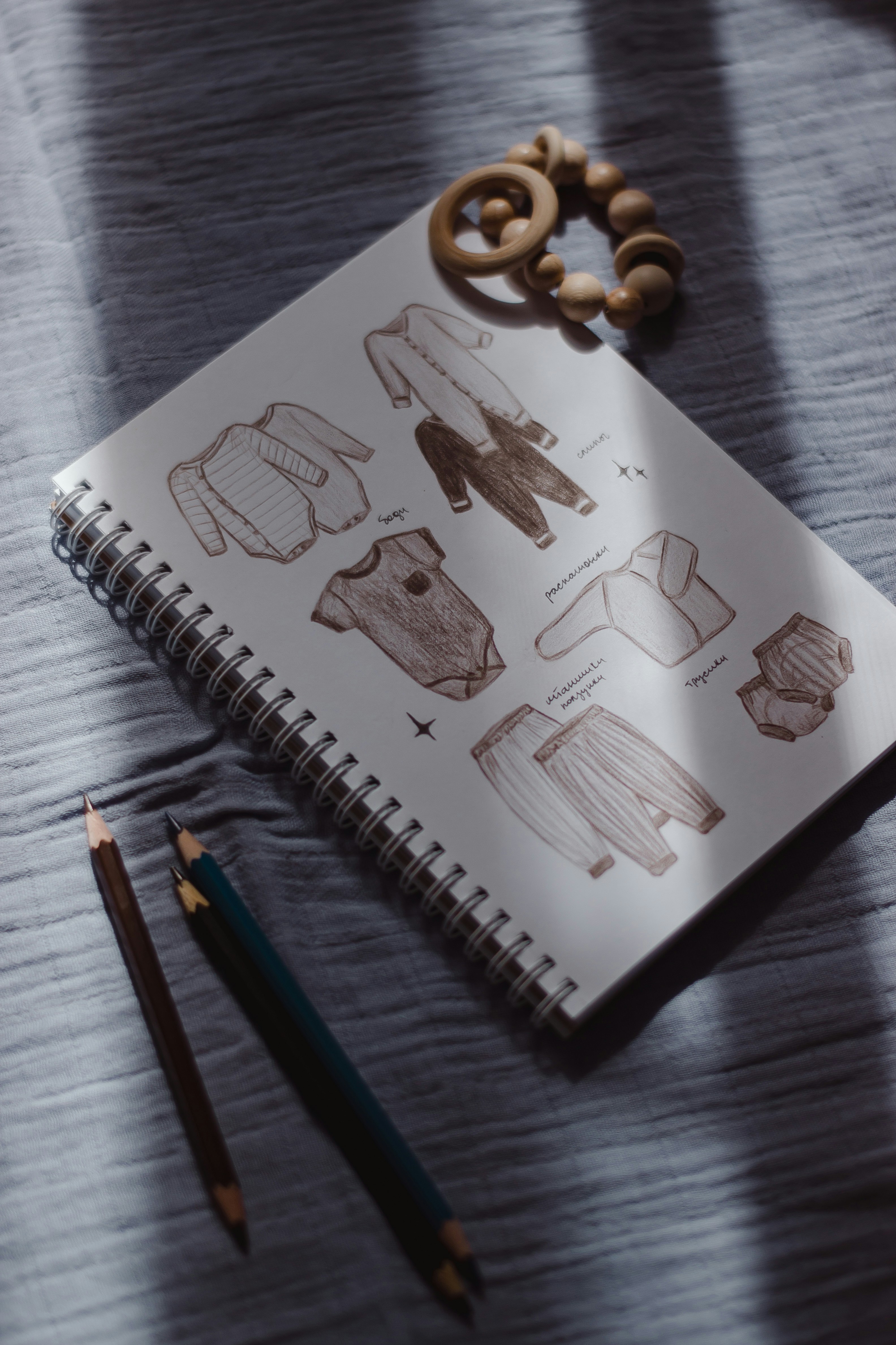 Fashion sketches of various clothing items displayed in a notebook, accompanied by colored pencils, showcasing the creative process of design.