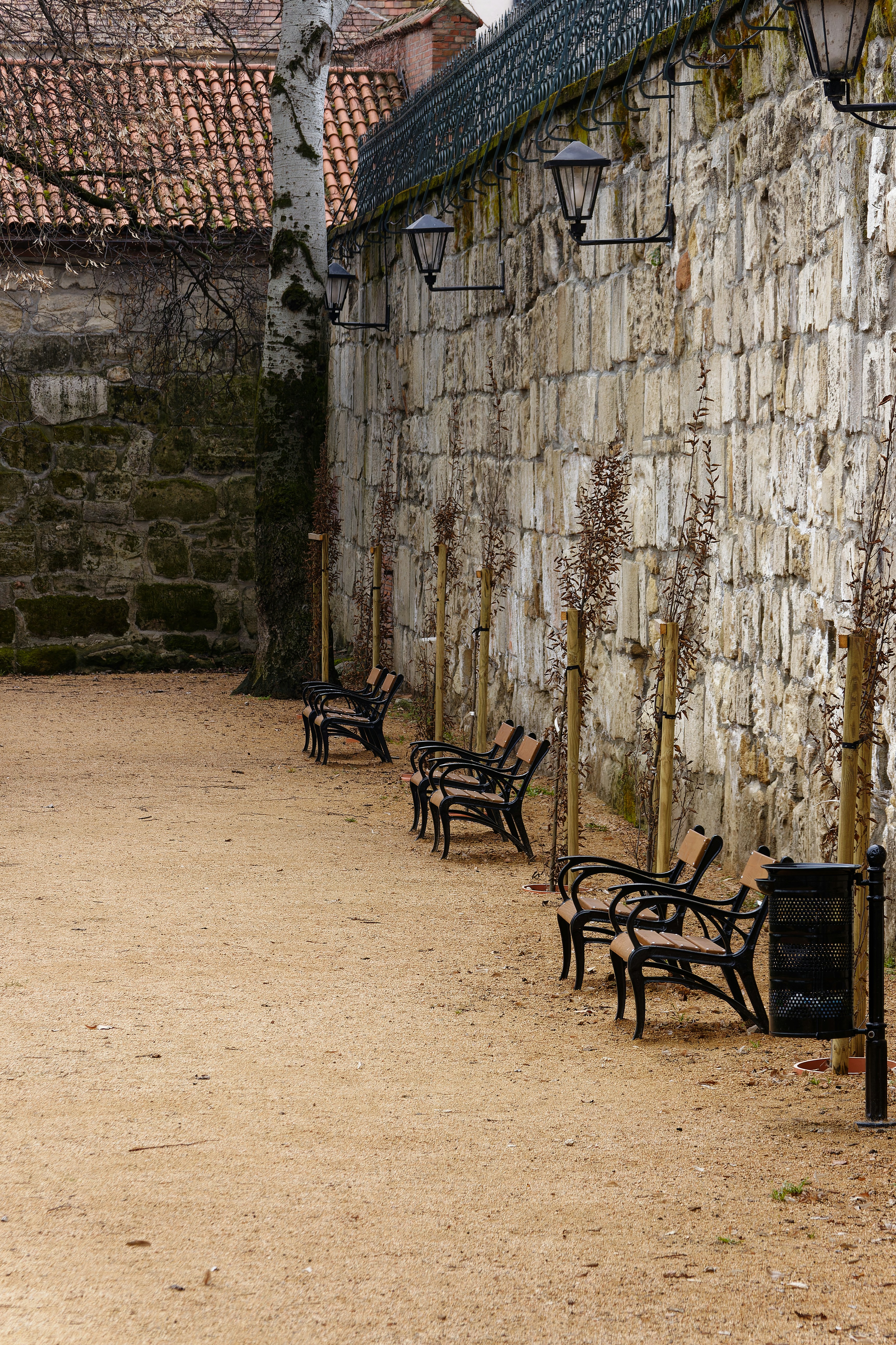 Row of Iron Benches Along a Weathered Stone Wall Under Lanterns