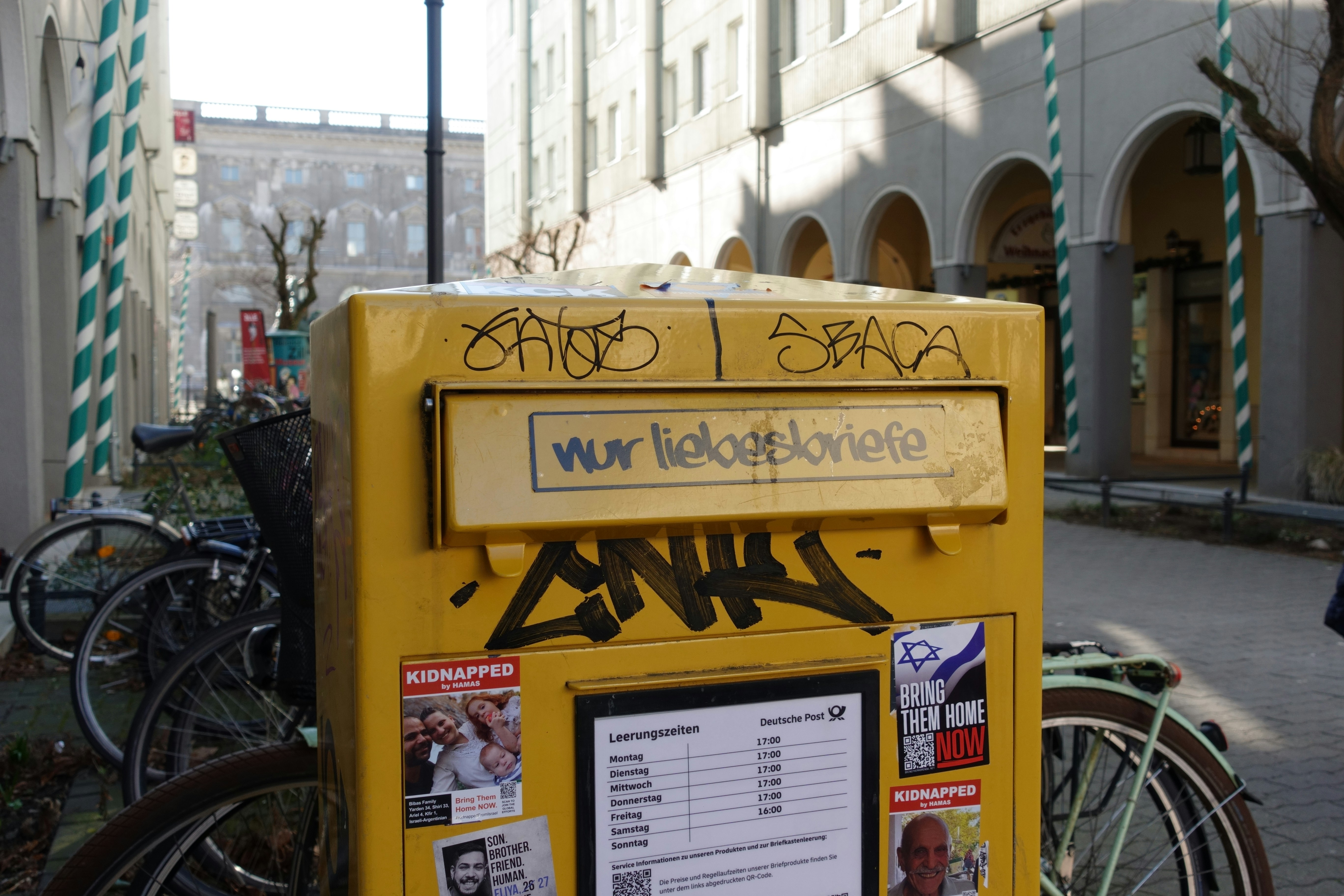 A vibrant yellow mailbox adorned with graffiti stands amidst parked bicycles in a lively urban alleyway.