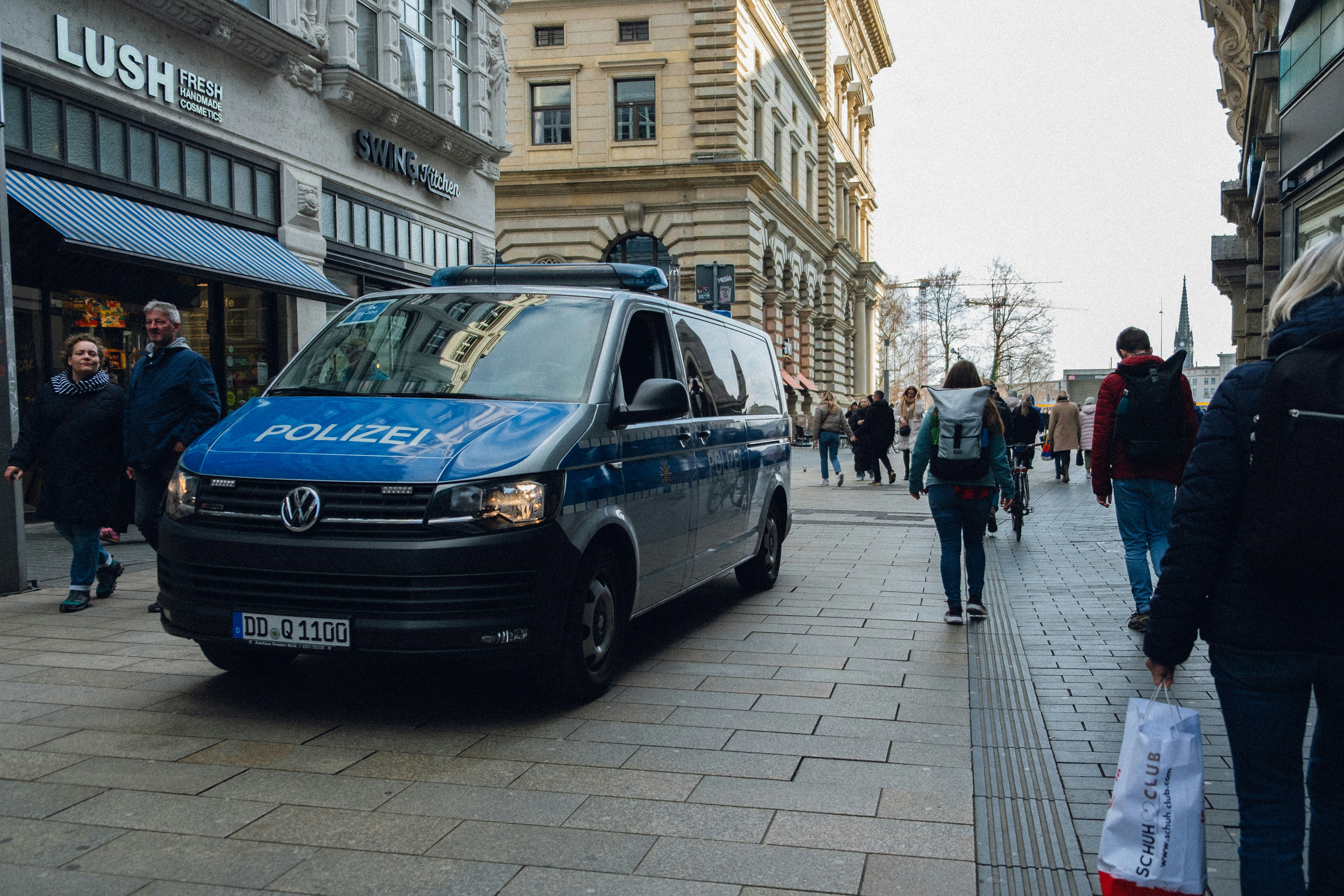 City street with a blue van and pedestrians in motion.