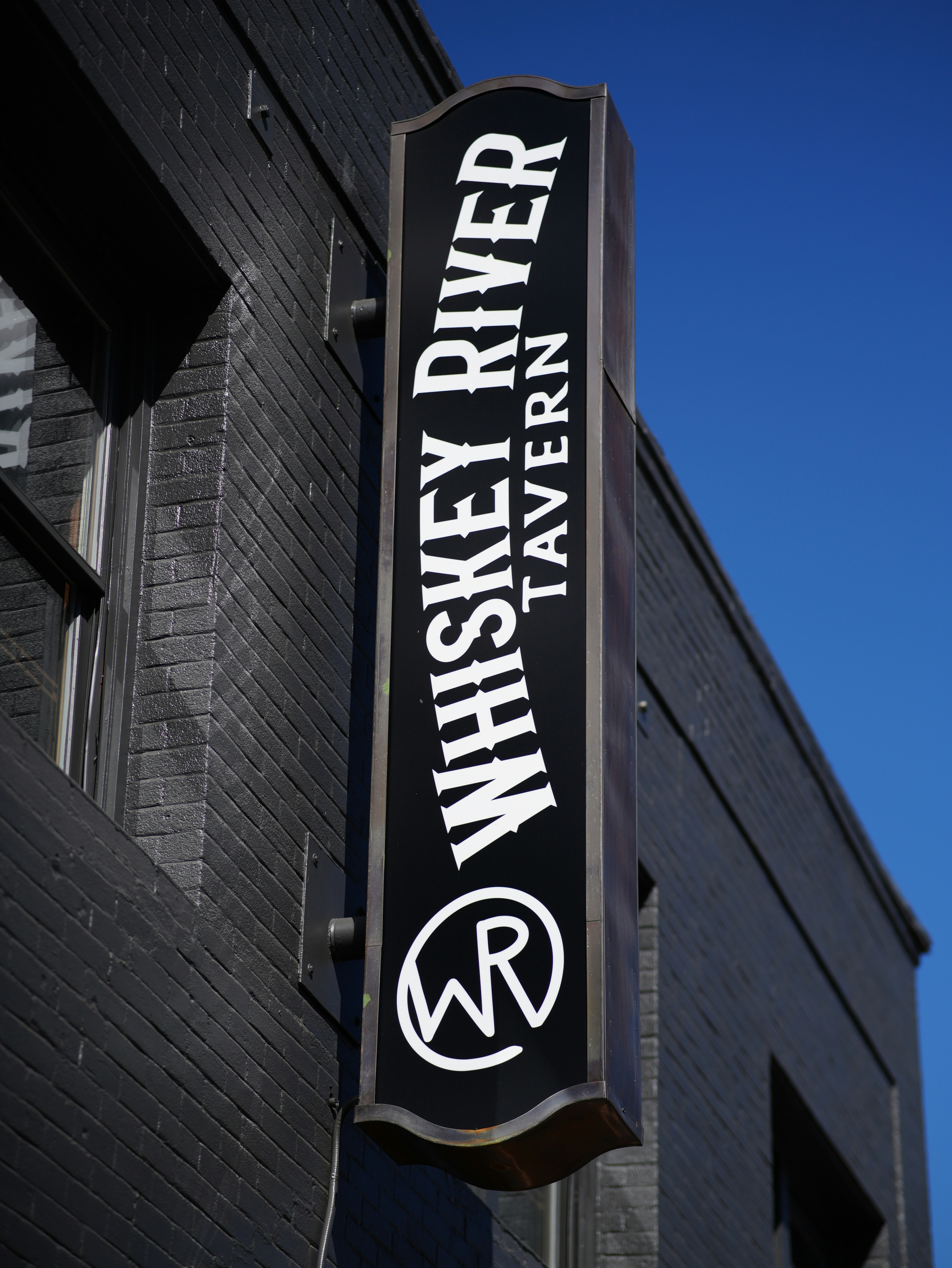 Vertical Beacon: Whiskey River Tavern Sign Adorning a Brick Facade