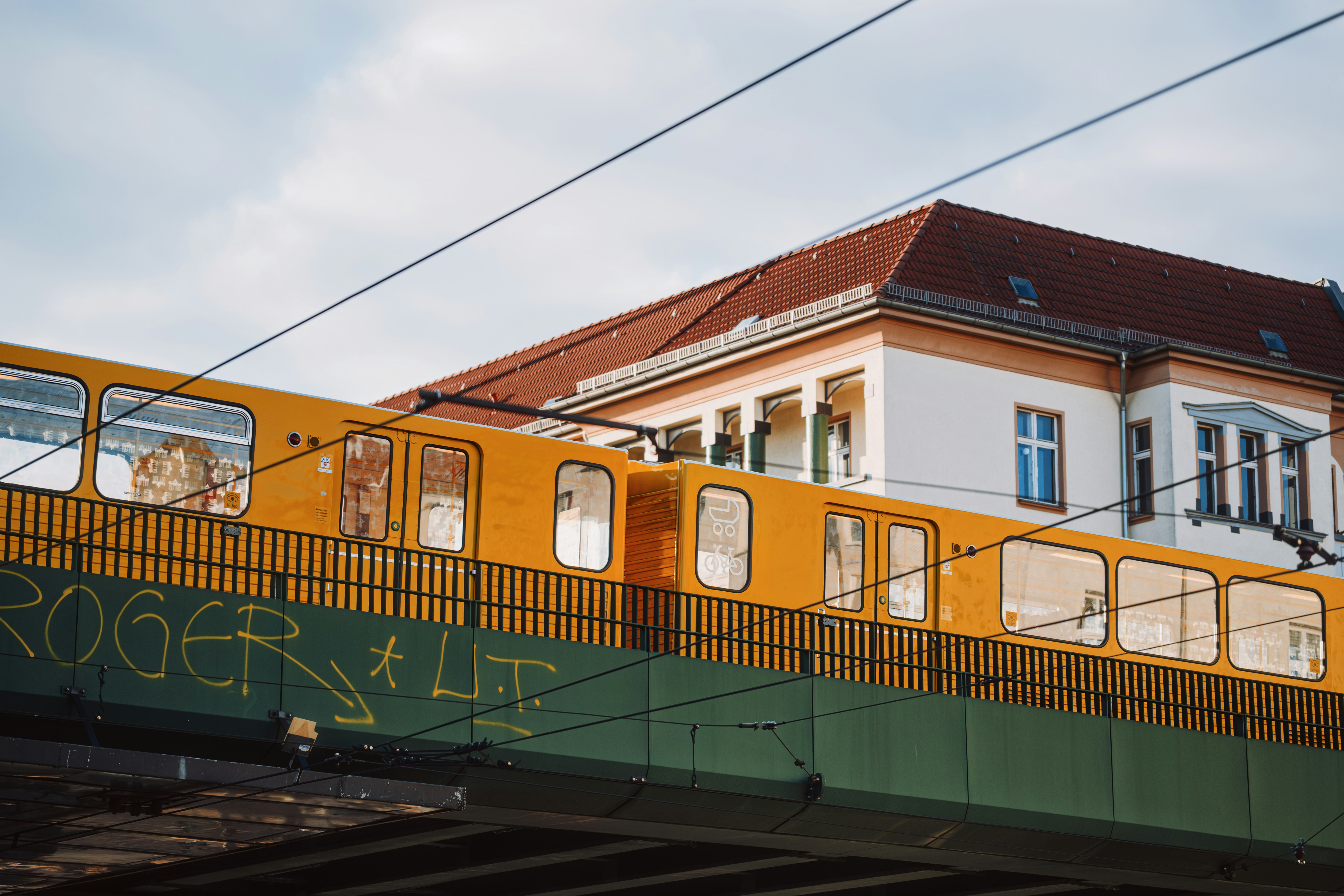 Yellow train crosses a green bridge with a background of a white building under a blue sky.