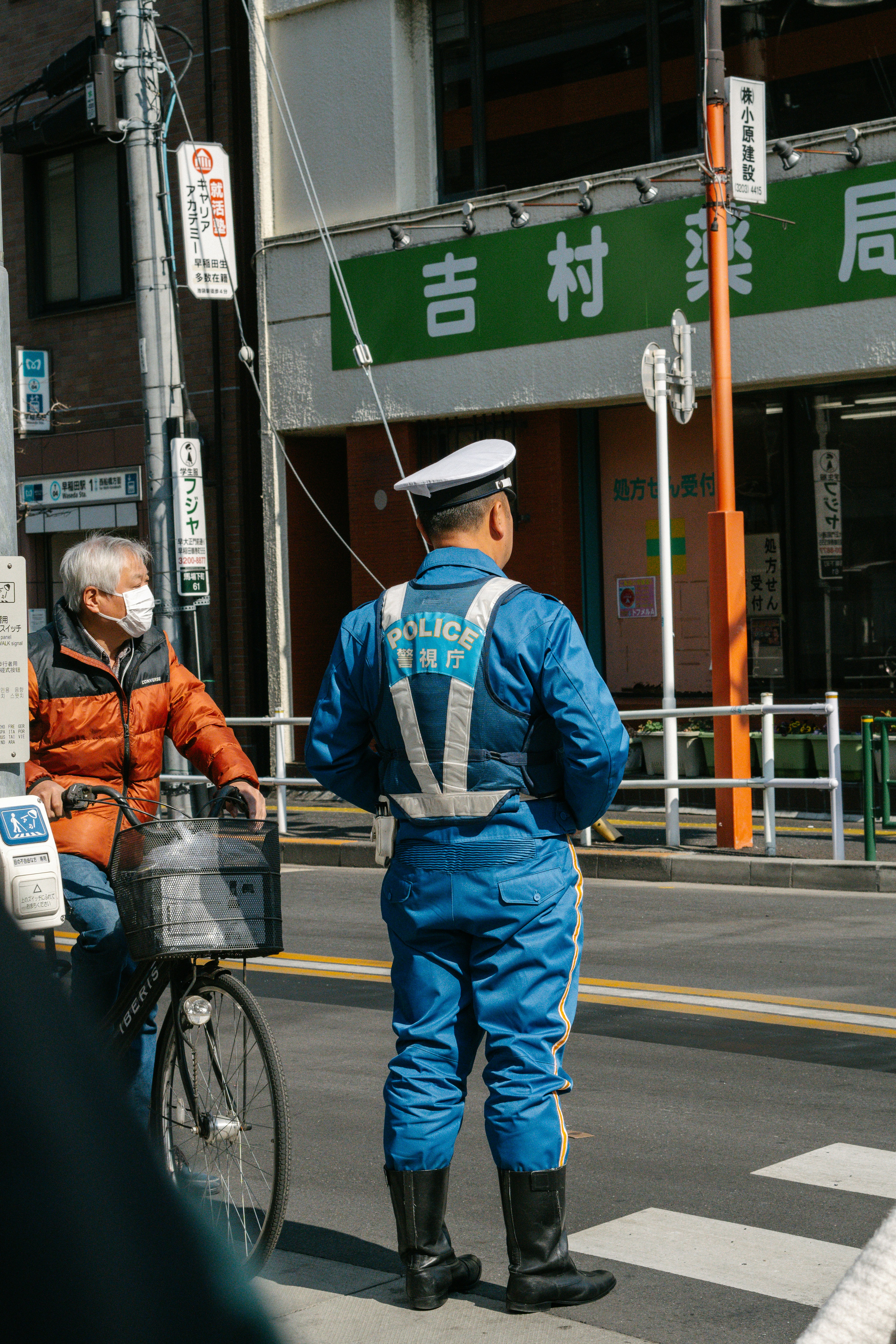 Blue‑Uniformed officer on a Japanese street, observed by a cyclist