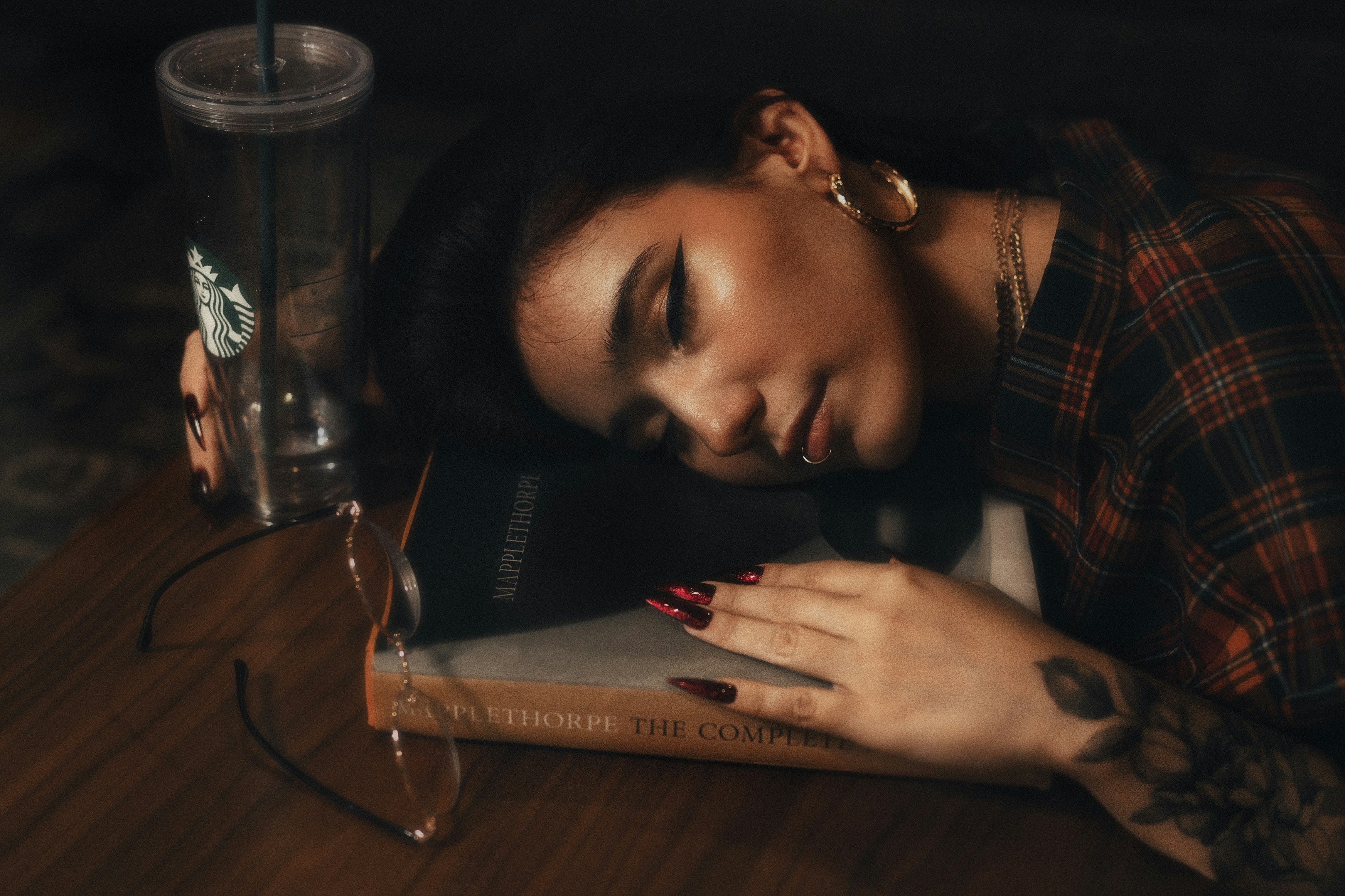 Young woman resting her head on a book, with a drink nearby, showcasing a moment of introspection and tranquility.